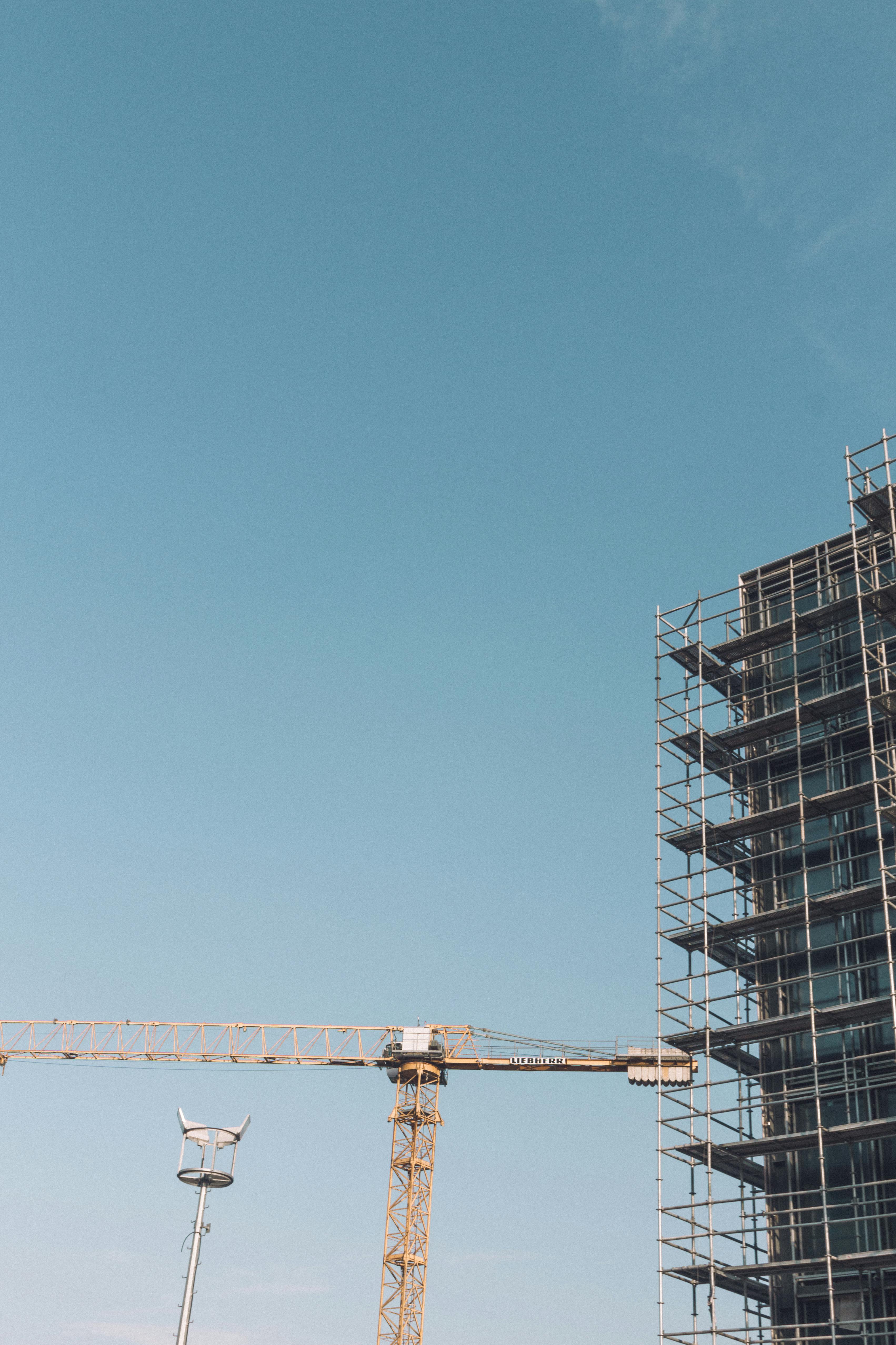Construction crane against building with scaffolding · Free Stock Photo