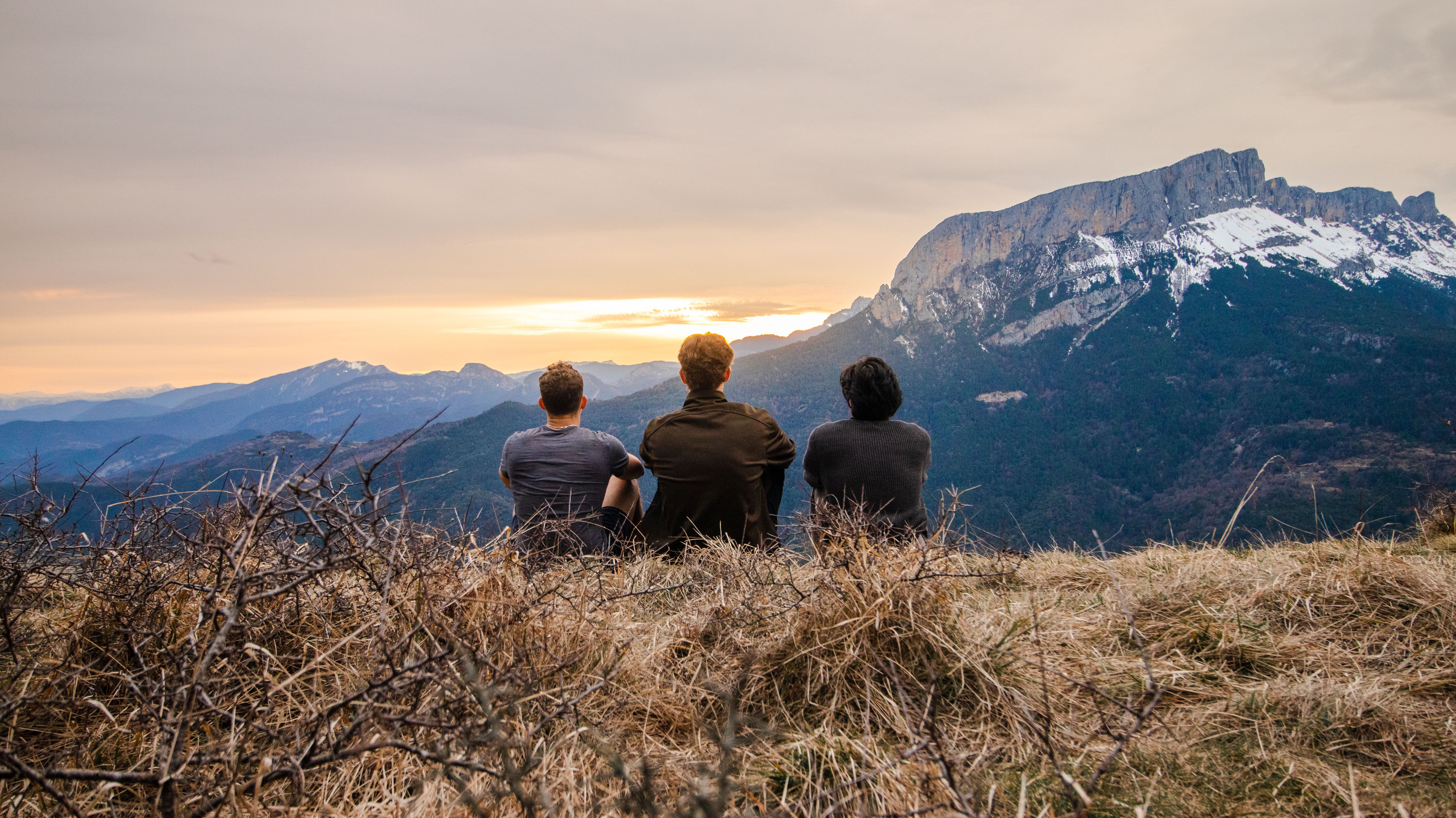 Men Sitting on Grass in Mountains at Sunset · Free Stock Photo