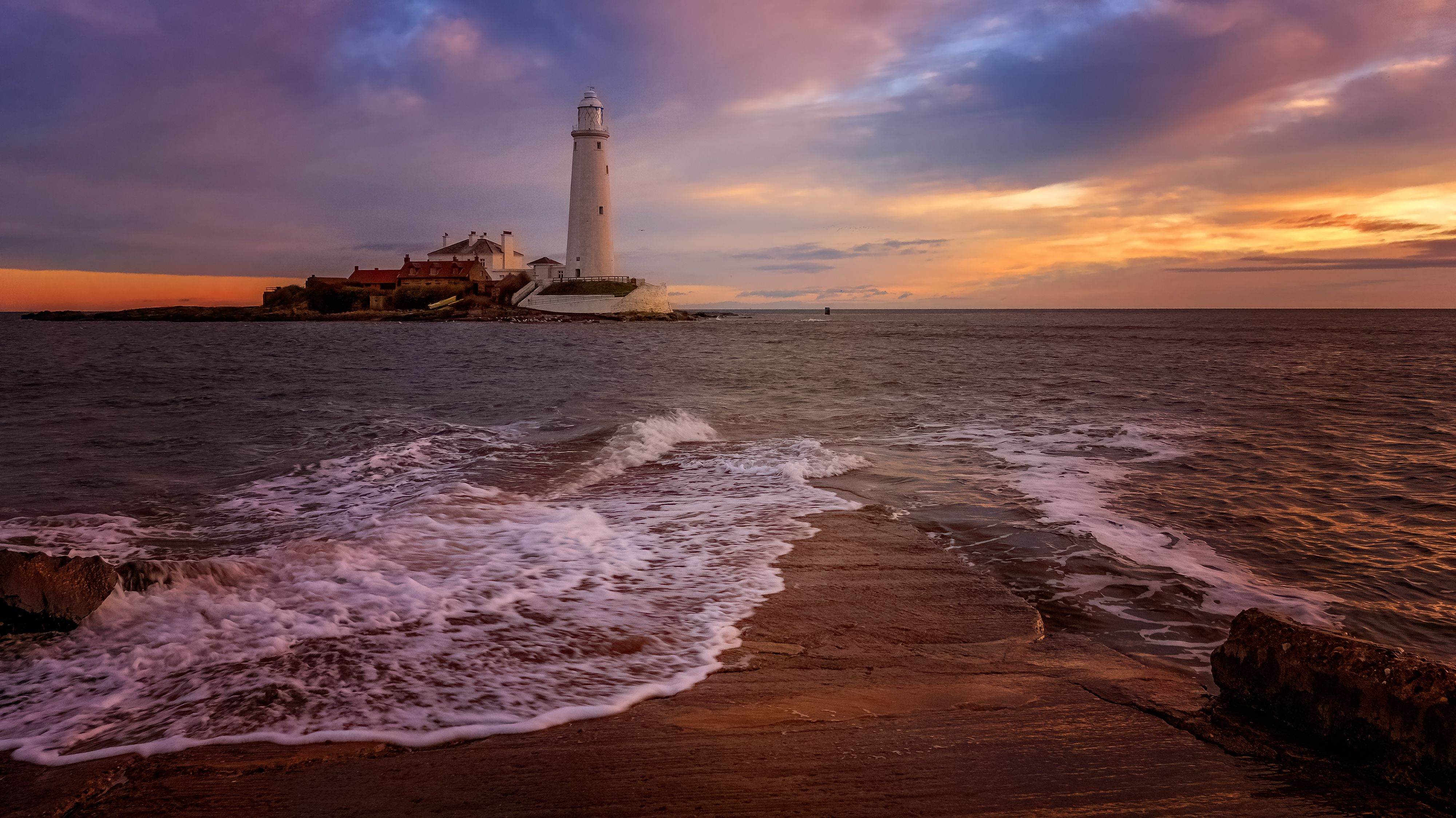 A lighthouse at sunset with waves crashing on the shore · Free Stock Photo