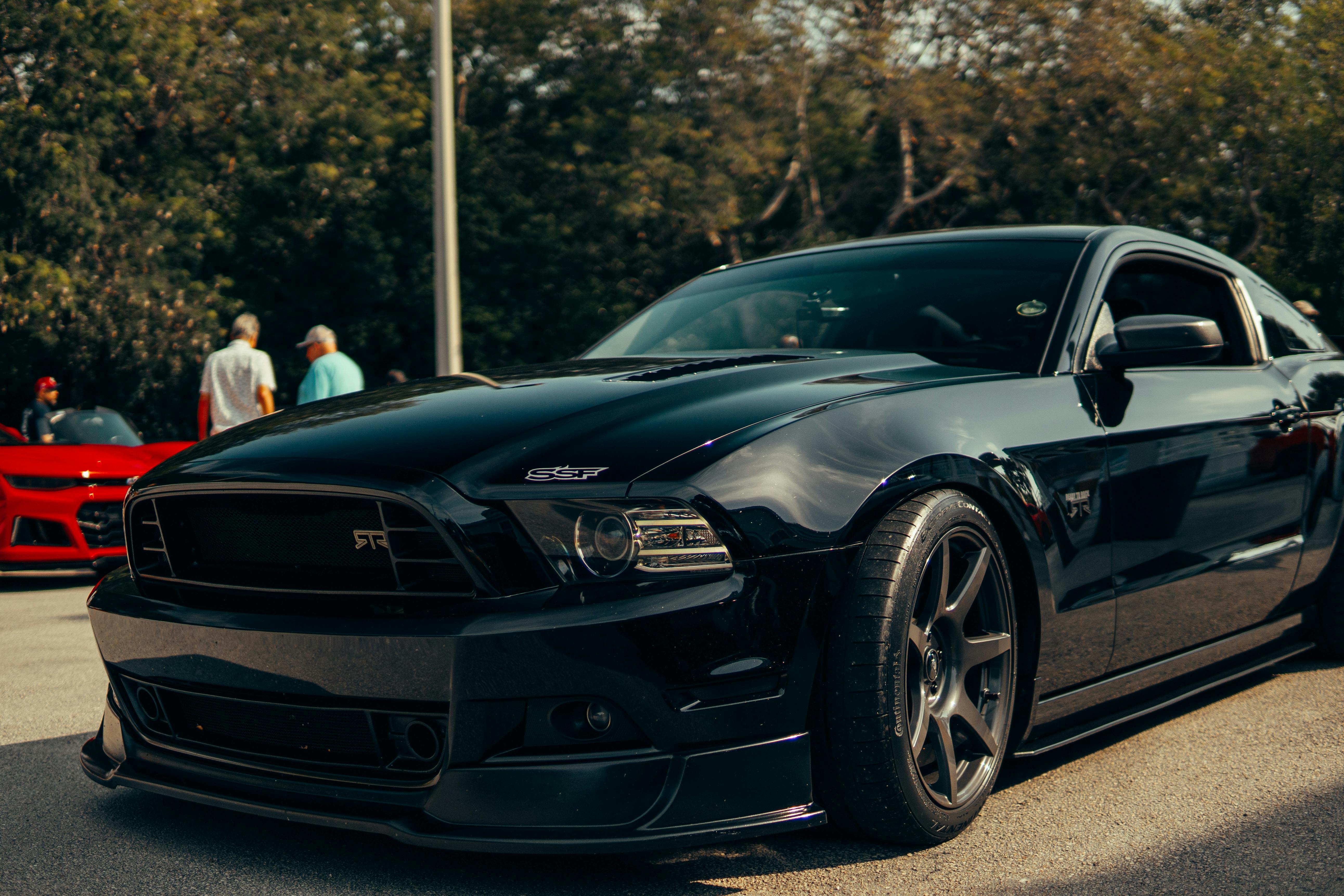 A black mustang parked in front of a crowd · Free Stock Photo