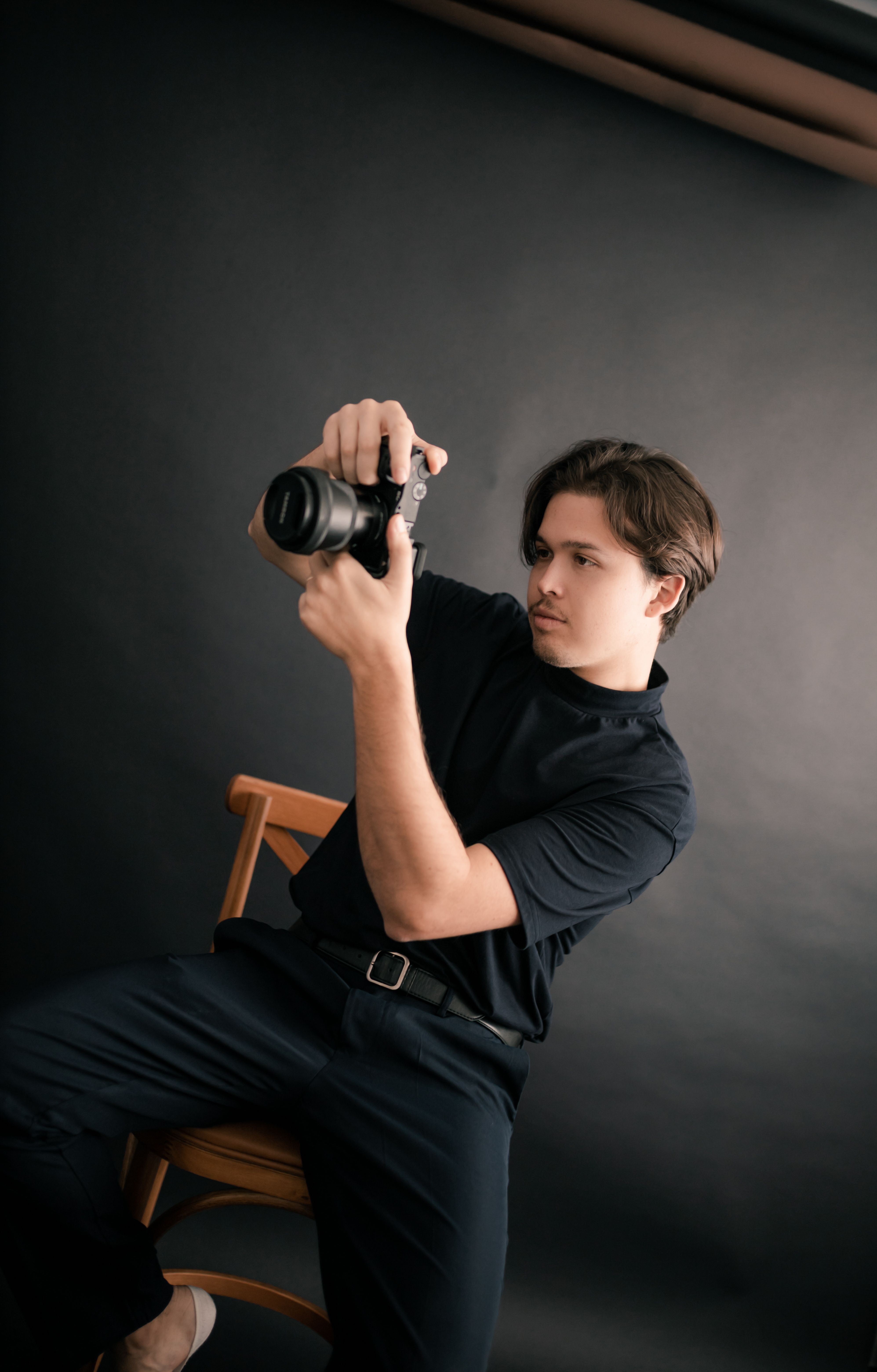 Man in Black Clothes Sitting on Chair and Taking Pictures with Camera ...