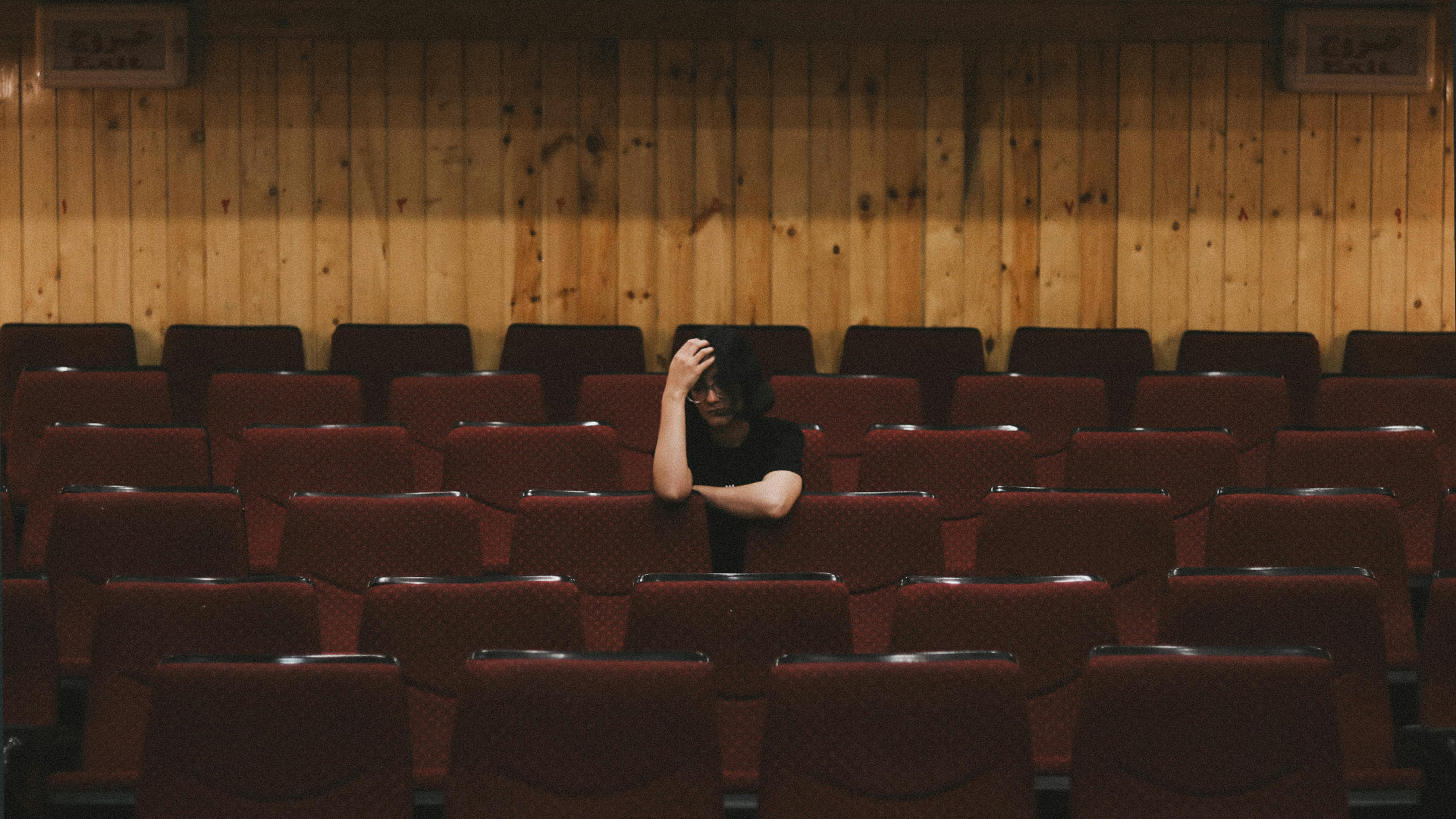 A Sad Person Sitting between Rows of Armchairs · Free Stock Photo