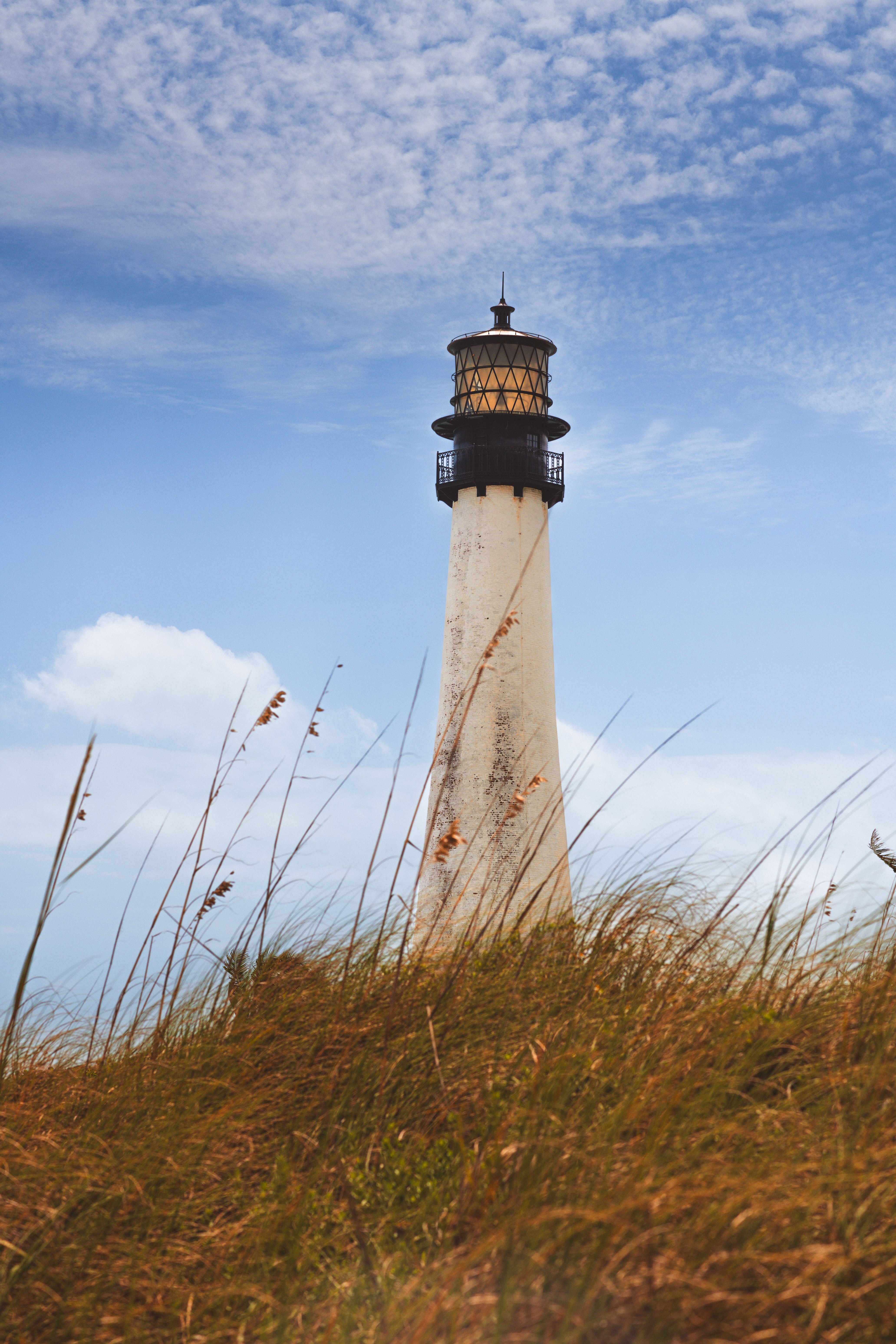 A lighthouse is shown in the grass with a blue sky · Free Stock Photo