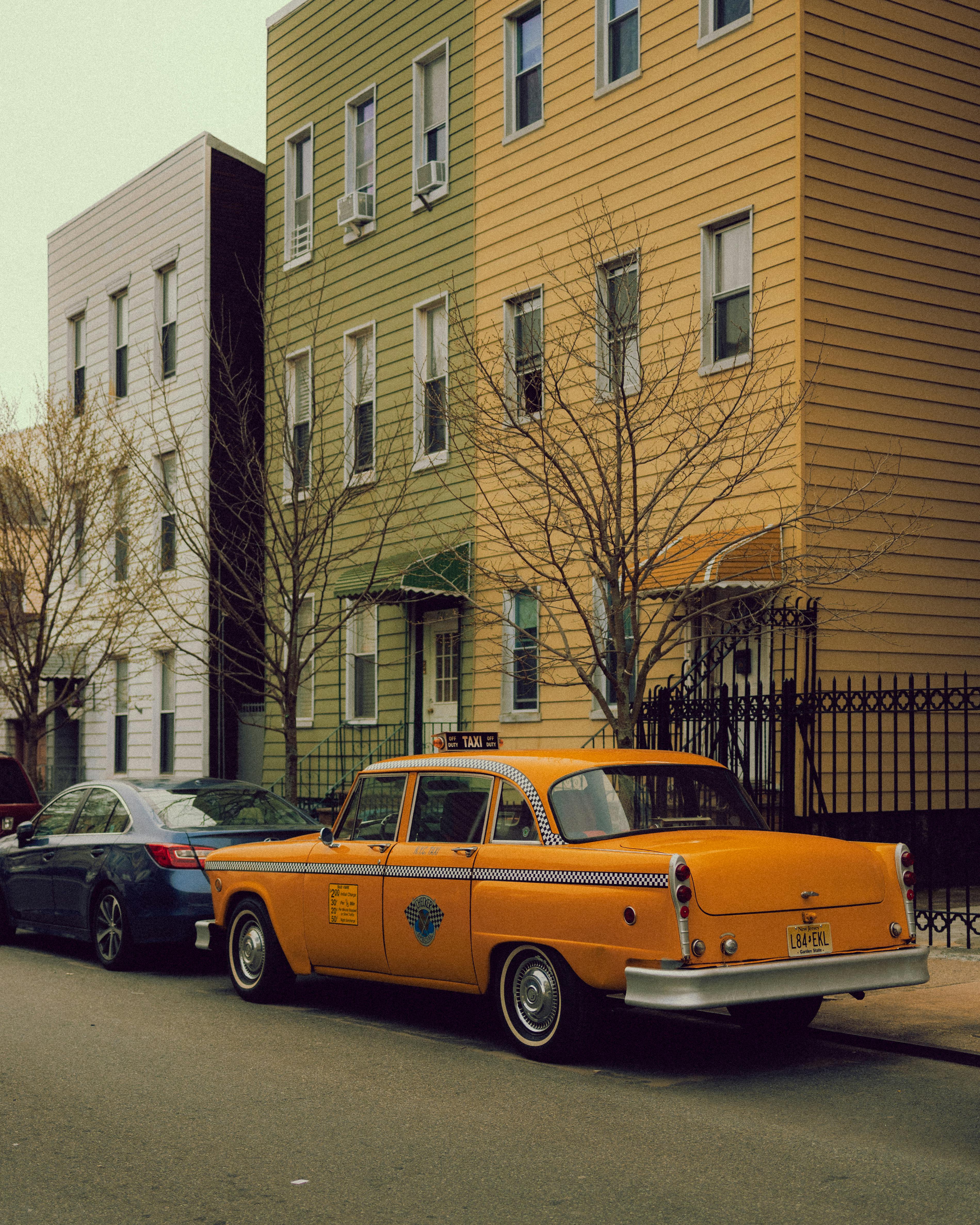 A yellow taxi parked in front of a row of houses · Free Stock Photo