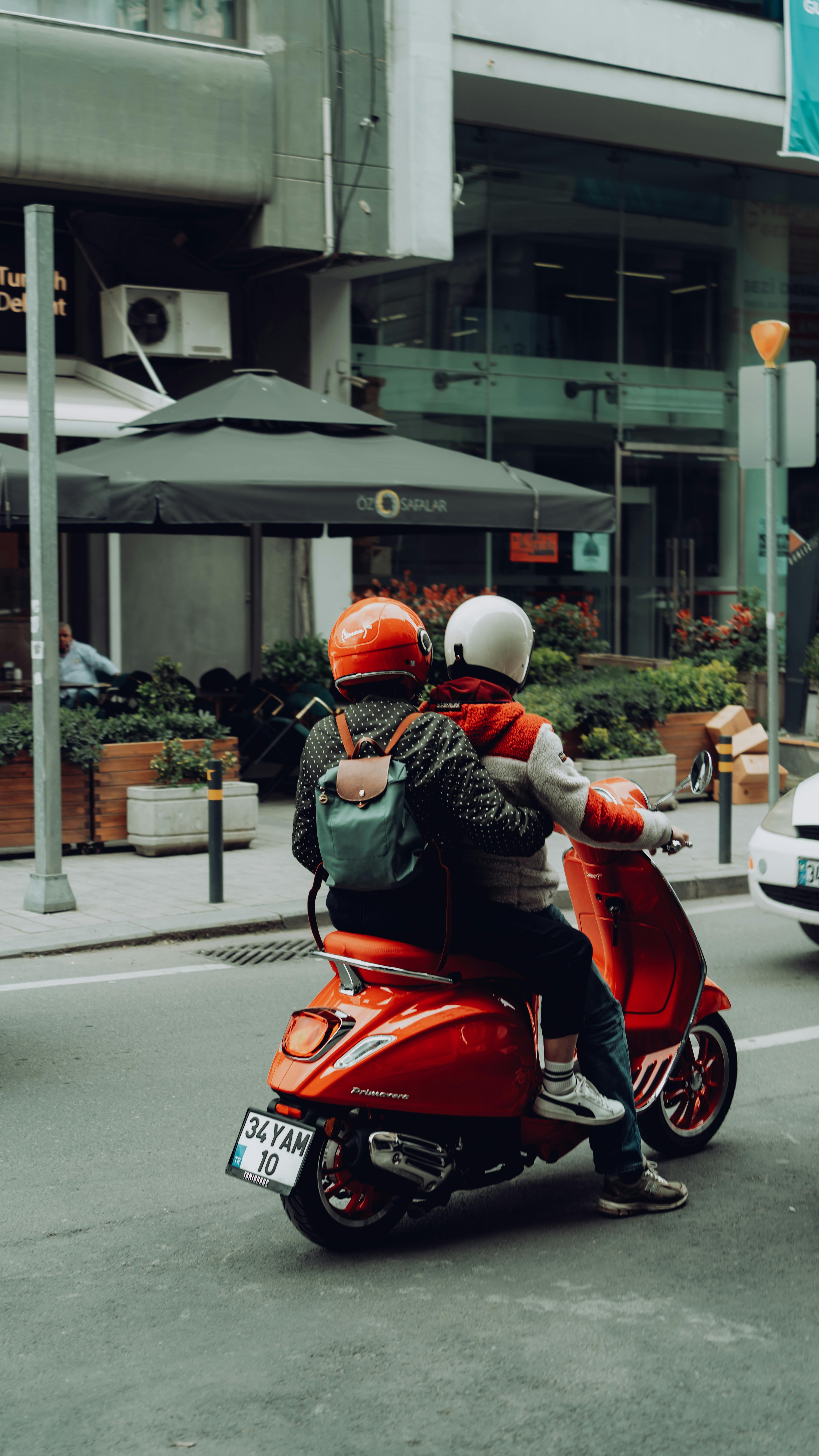 A couple riding a moped on a city street · Free Stock Photo