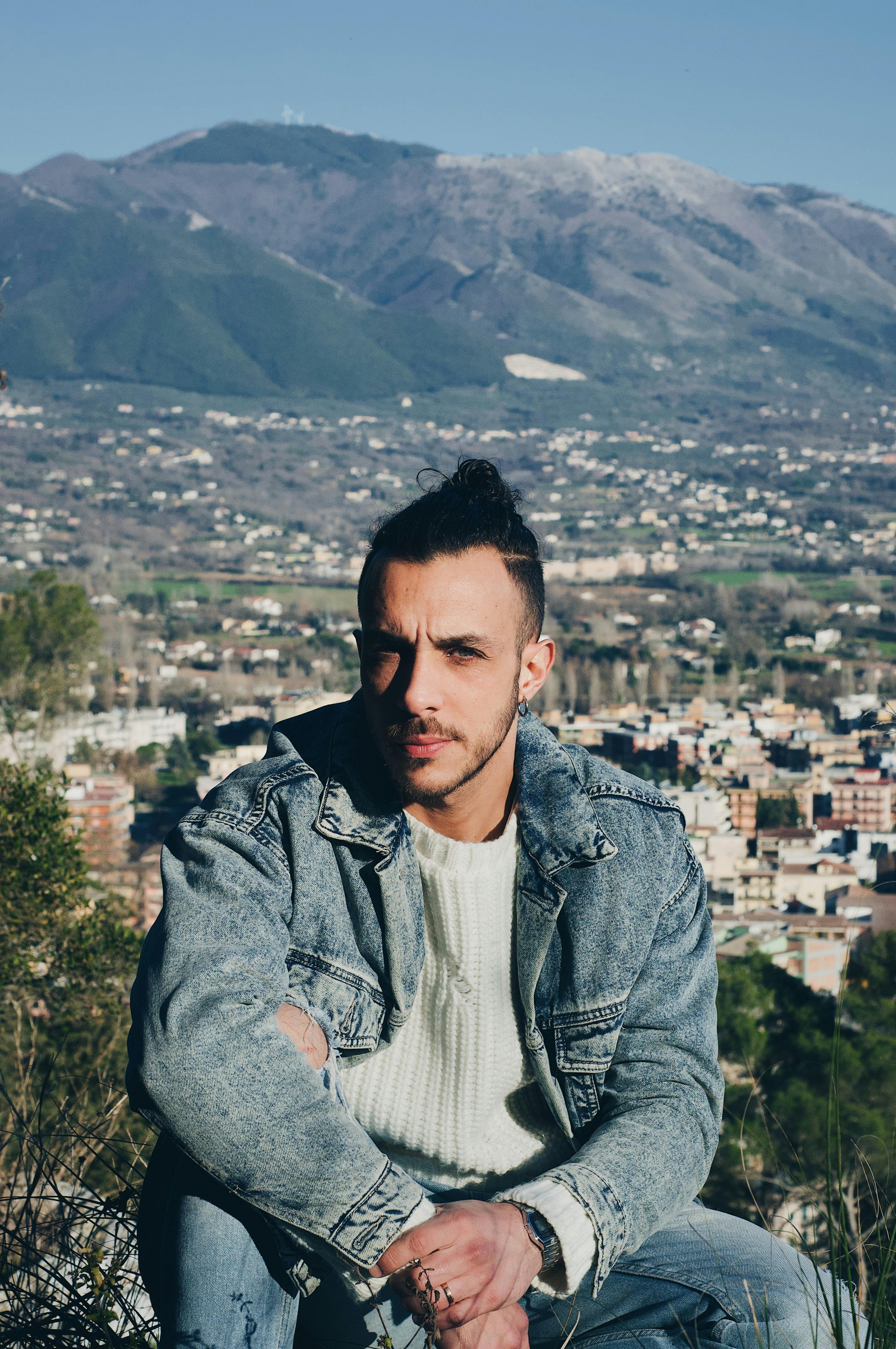 Man in Denim Crouching against Cityscape · Free Stock Photo