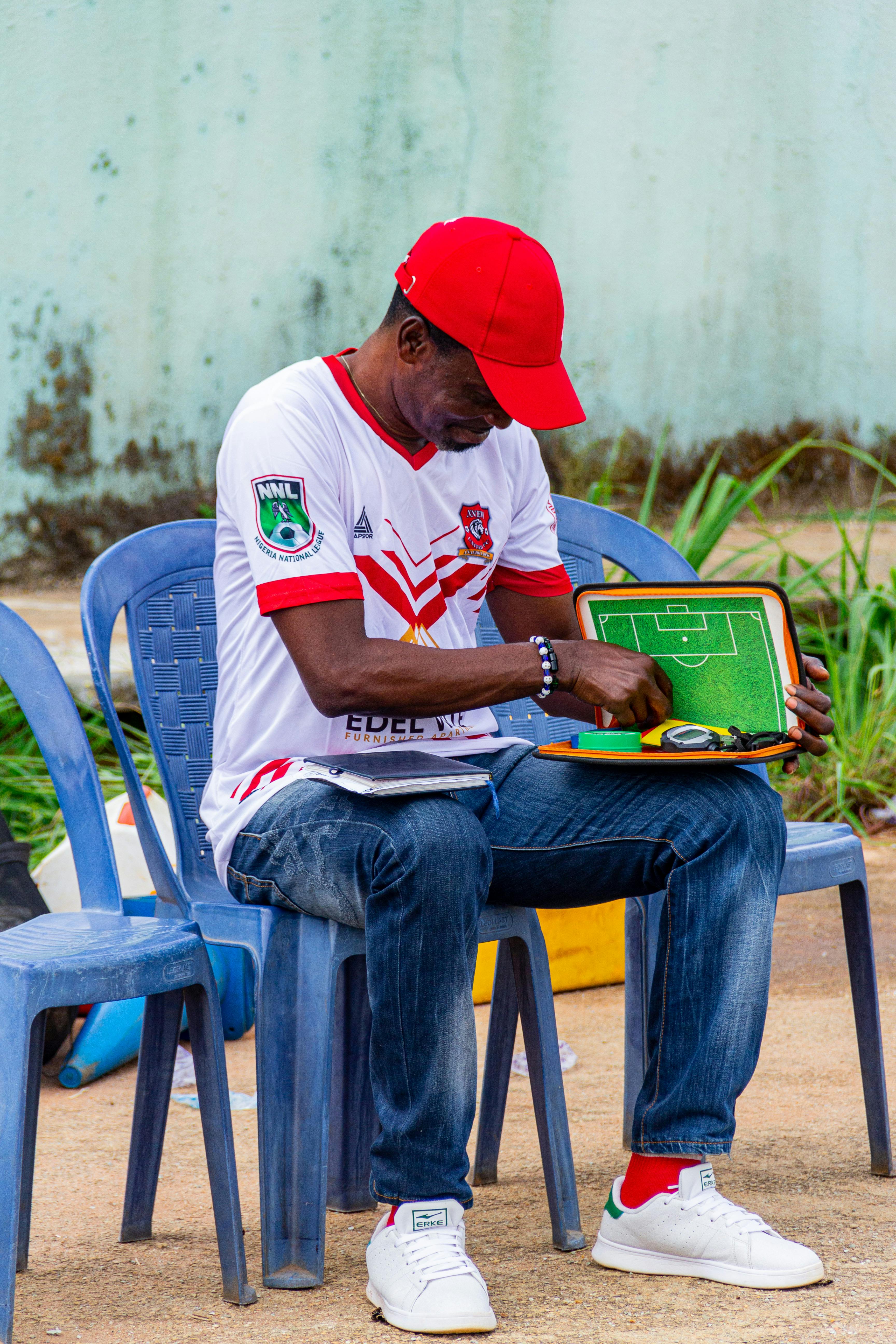Man Wearing a Red Baseball Cap Sitting Outdoors with a Pouch in Hands ...
