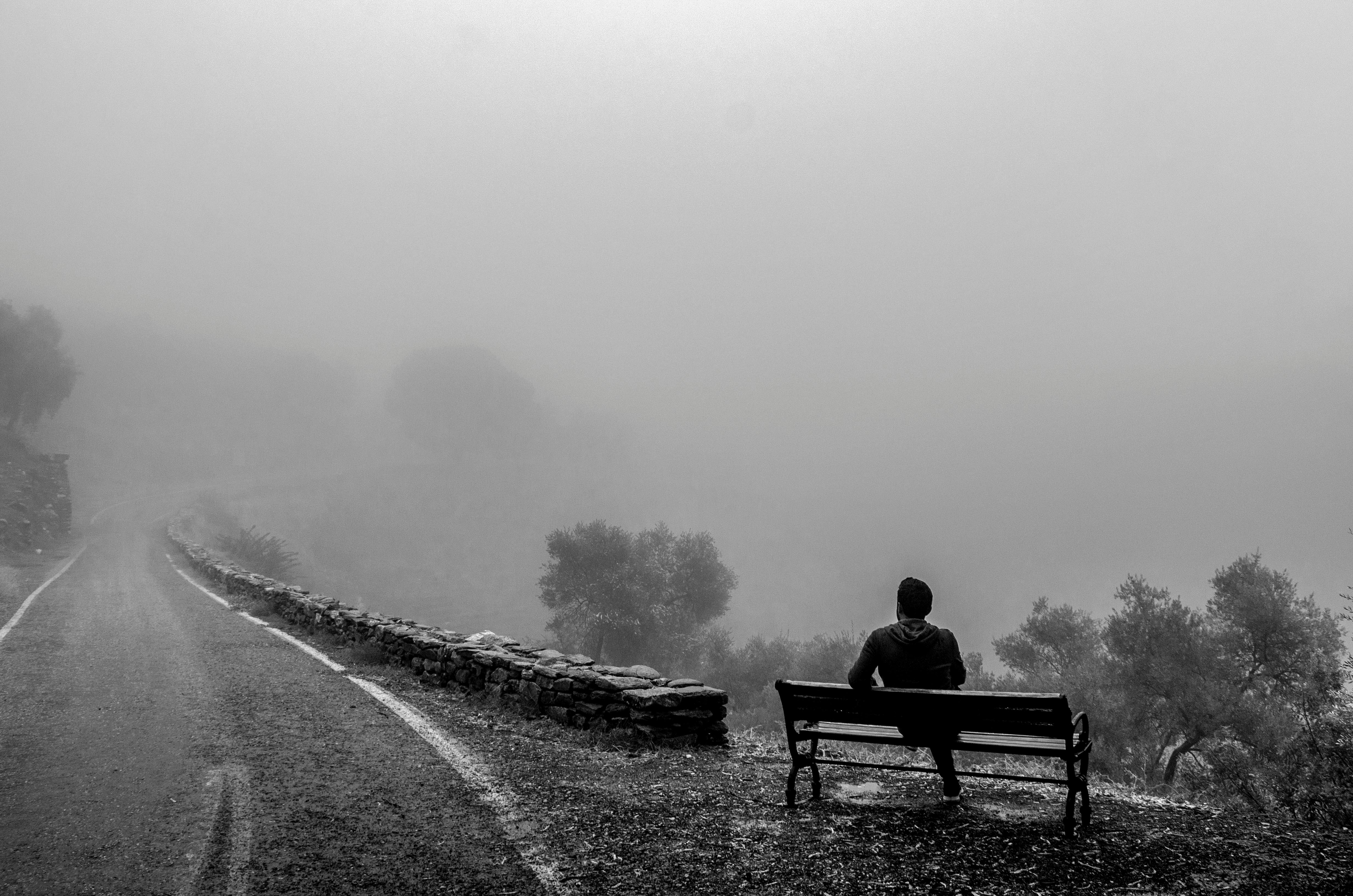 Man Sitting on Bench by the Road in Black and White · Free Stock Photo