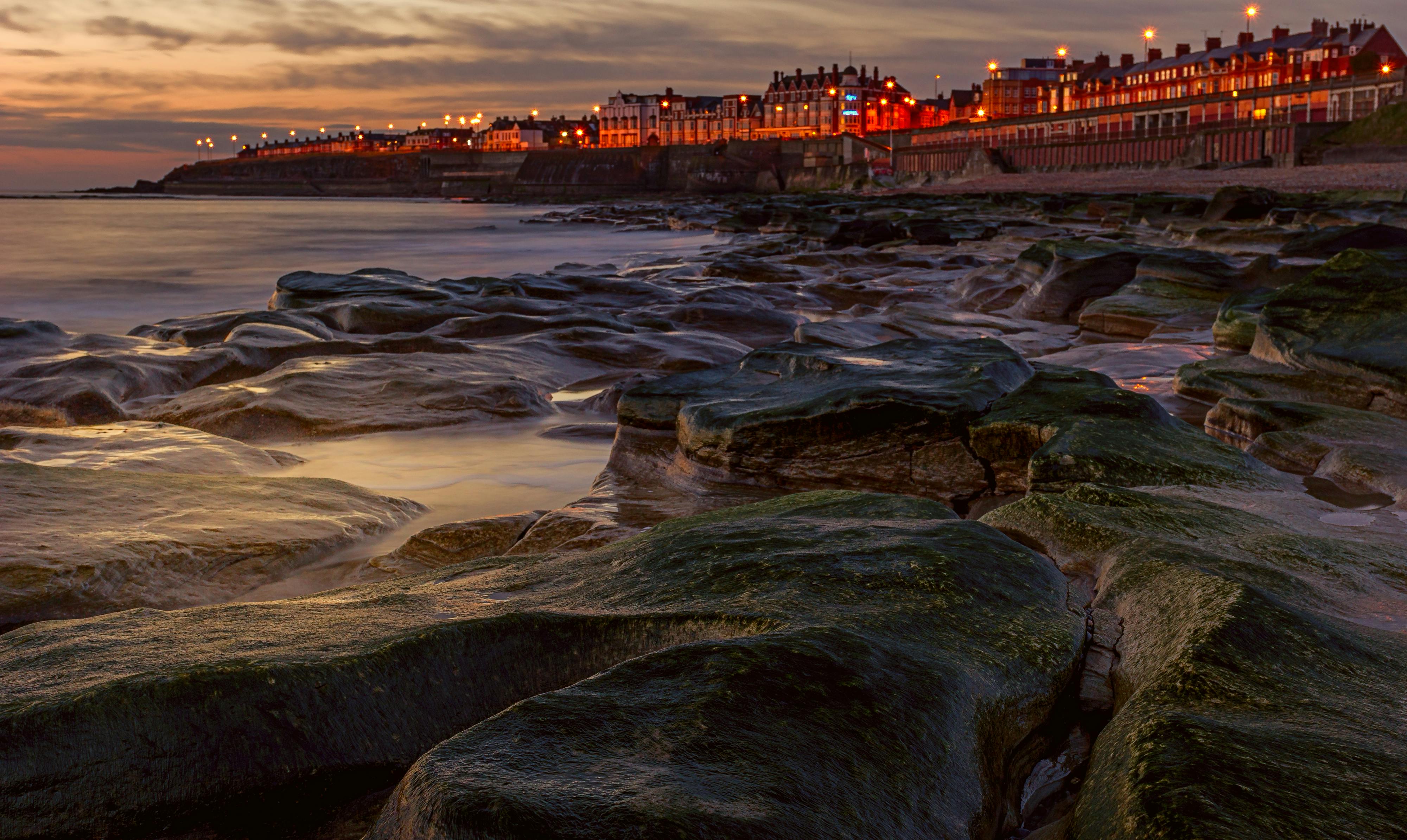 Dark Seashore with Stones, and an Illuminated Waterfront · Free Stock Photo