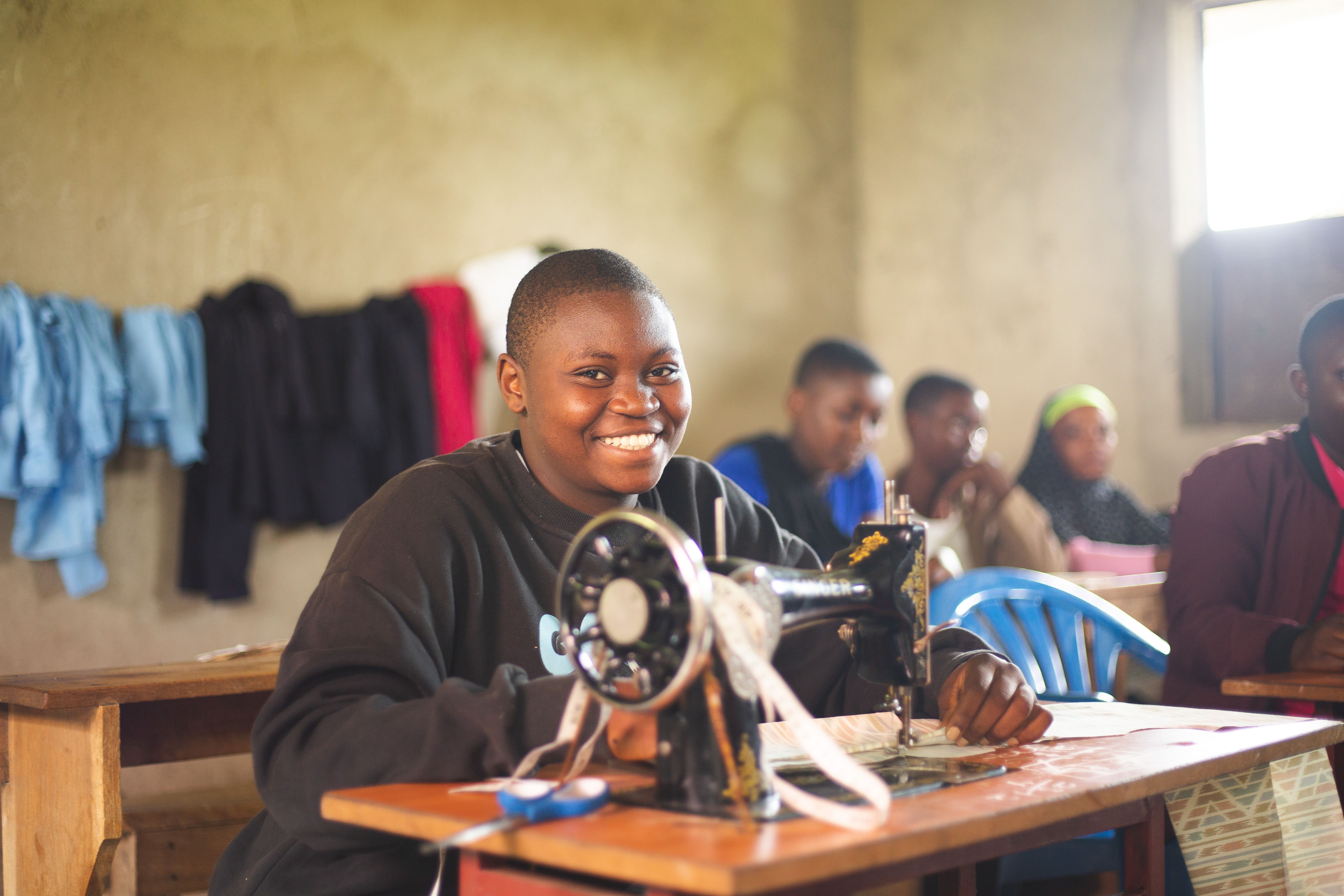 A young boy smiles while sewing at a sewing machine · Free Stock Photo