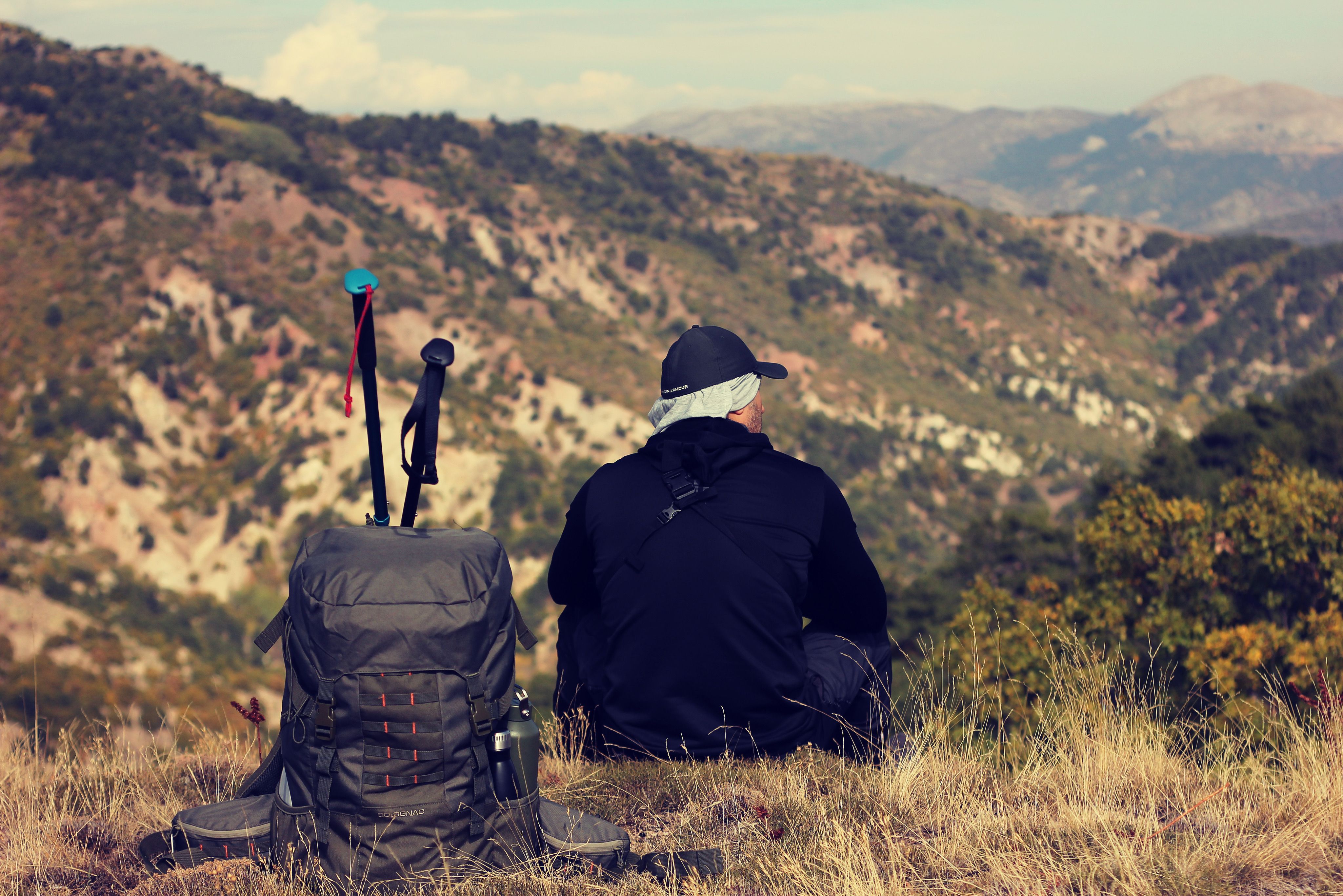 Back View of a Man with a Backpack Sitting on the Ground and Looking at ...