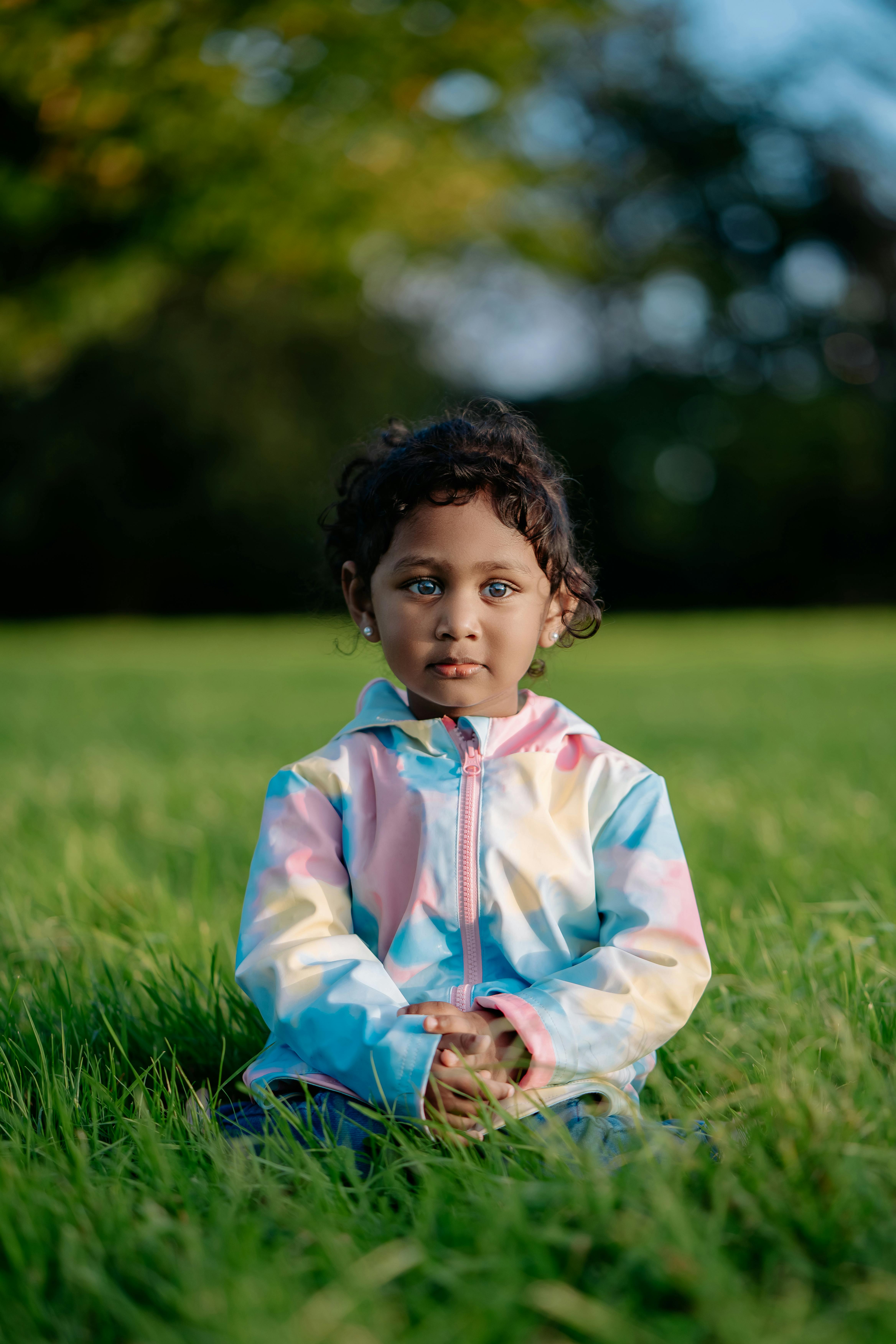 Little Girl in Pastel Jacket Sitting on Grass · Free Stock Photo