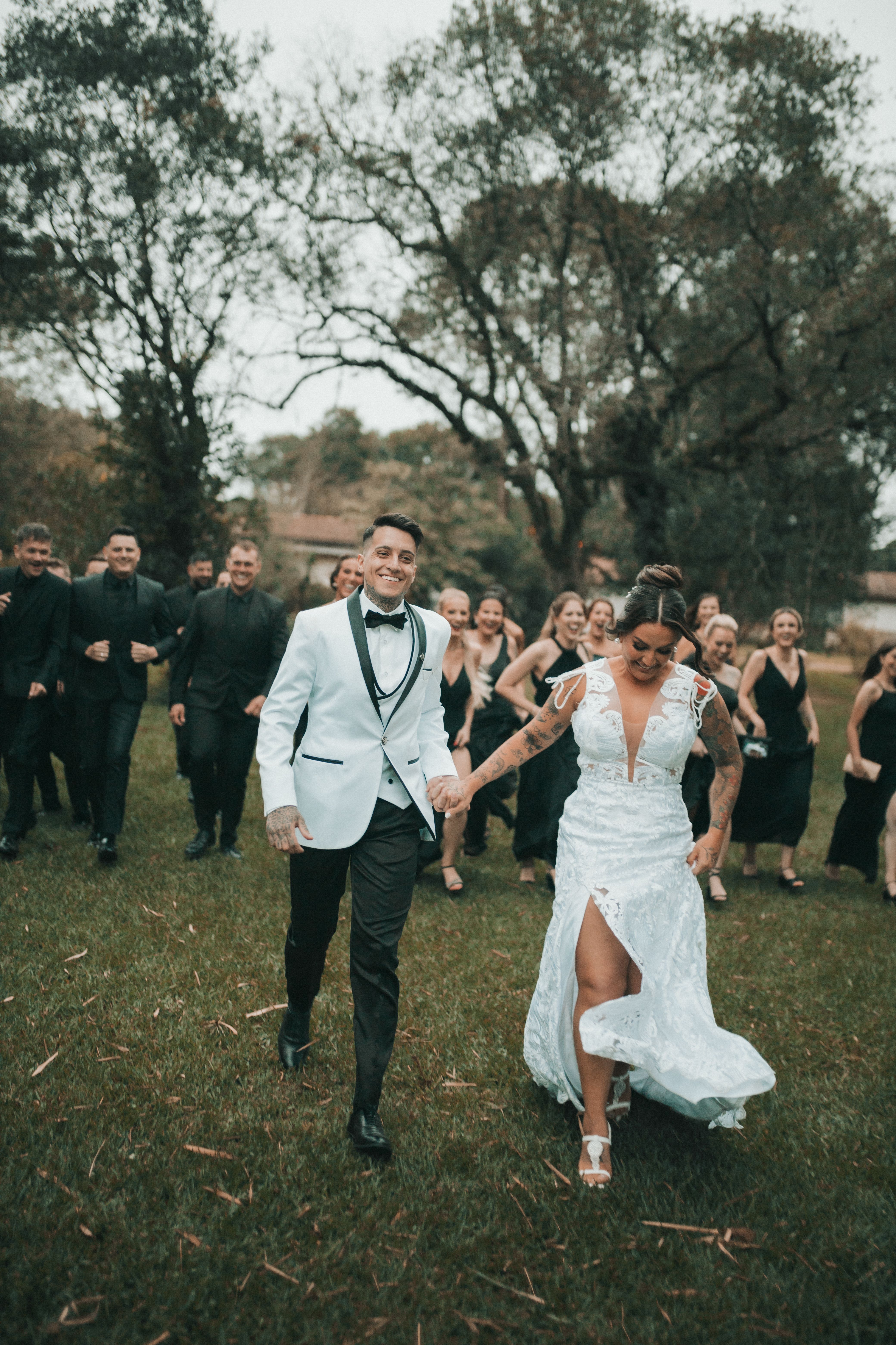Newlyweds Walking across Grass Field with Guests in Backg · Free Stock ...