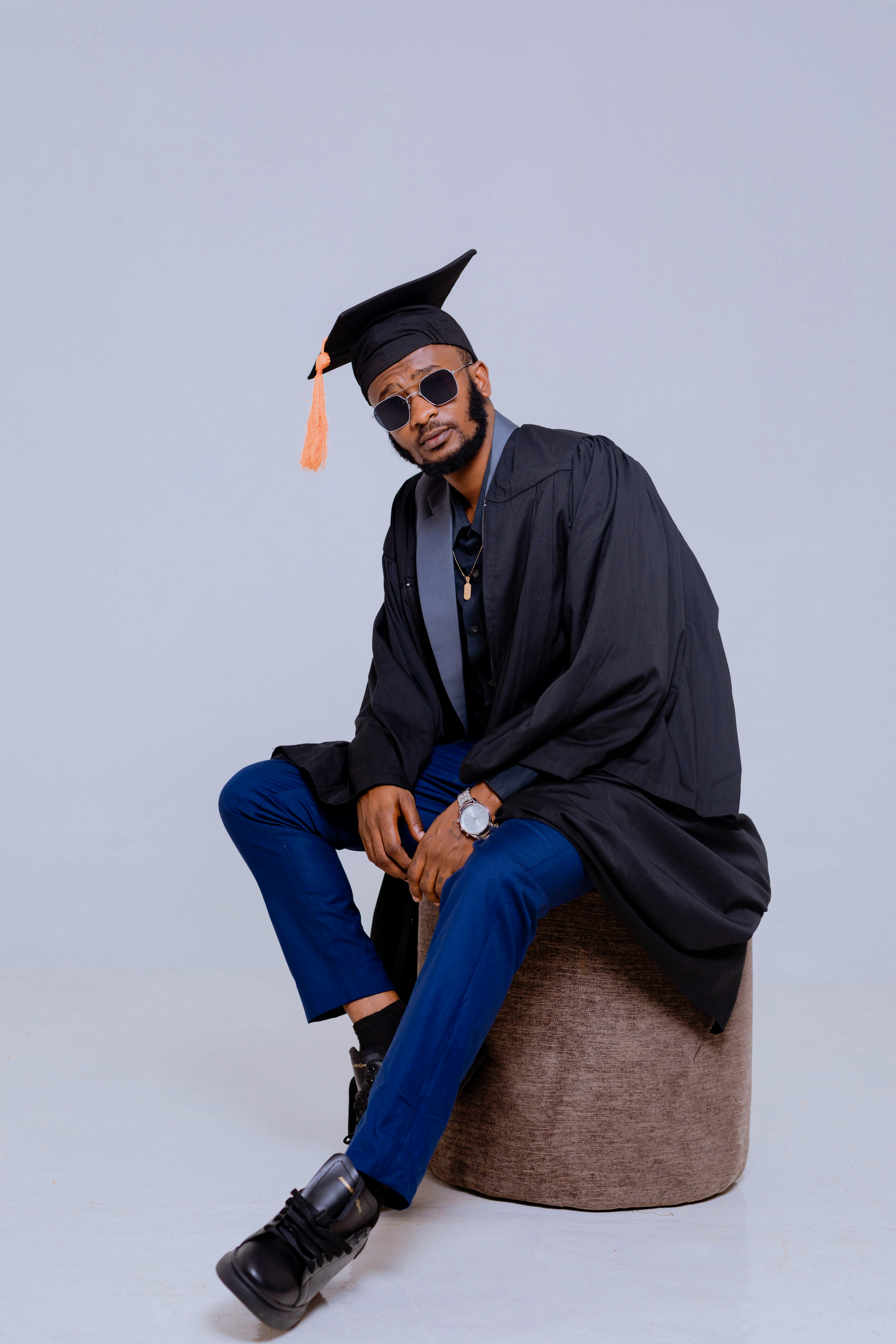 A man in graduation cap and gown sitting on a stool · Free Stock Photo