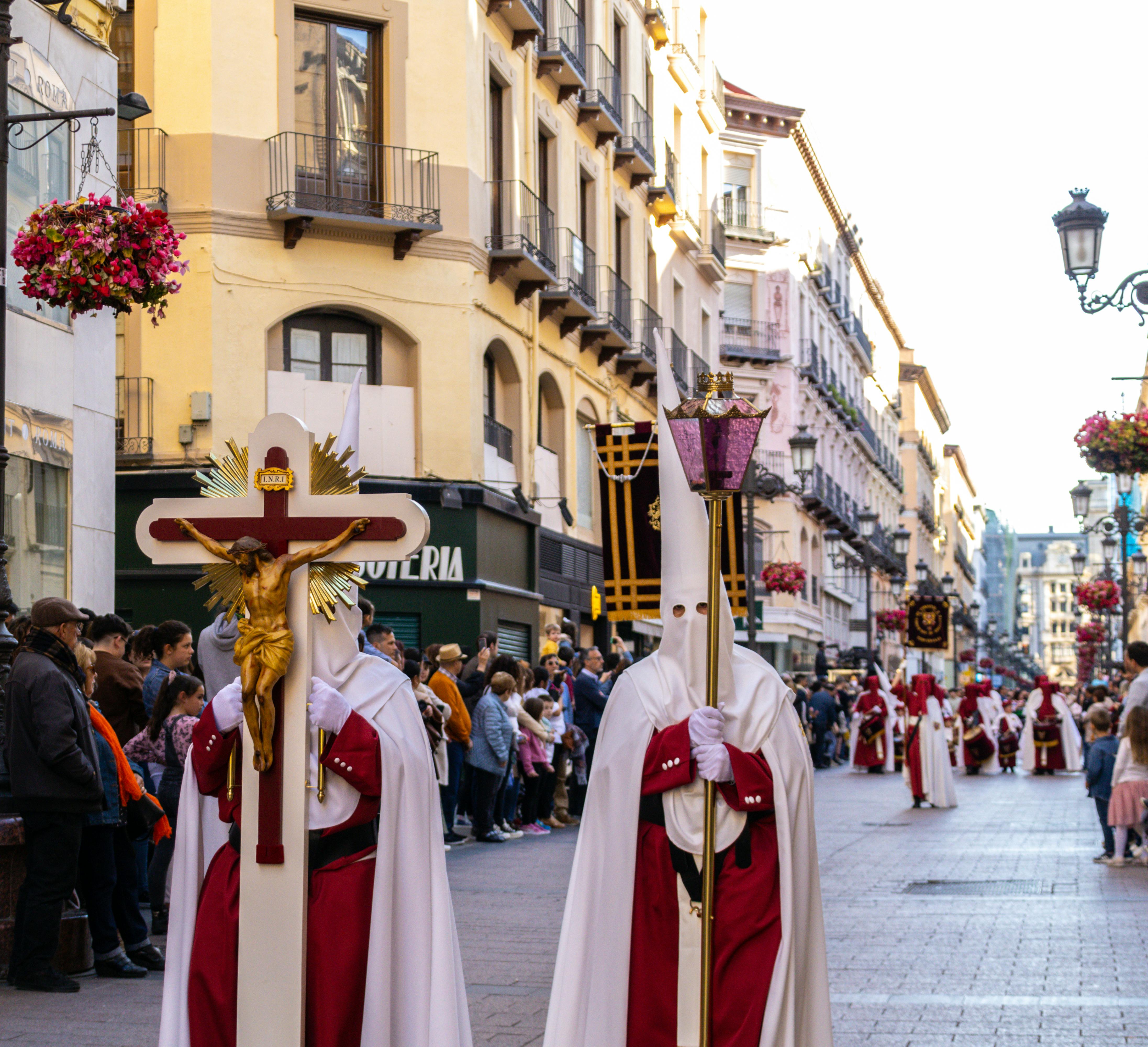 Two people dressed in white robes and crosses walking down a street ...