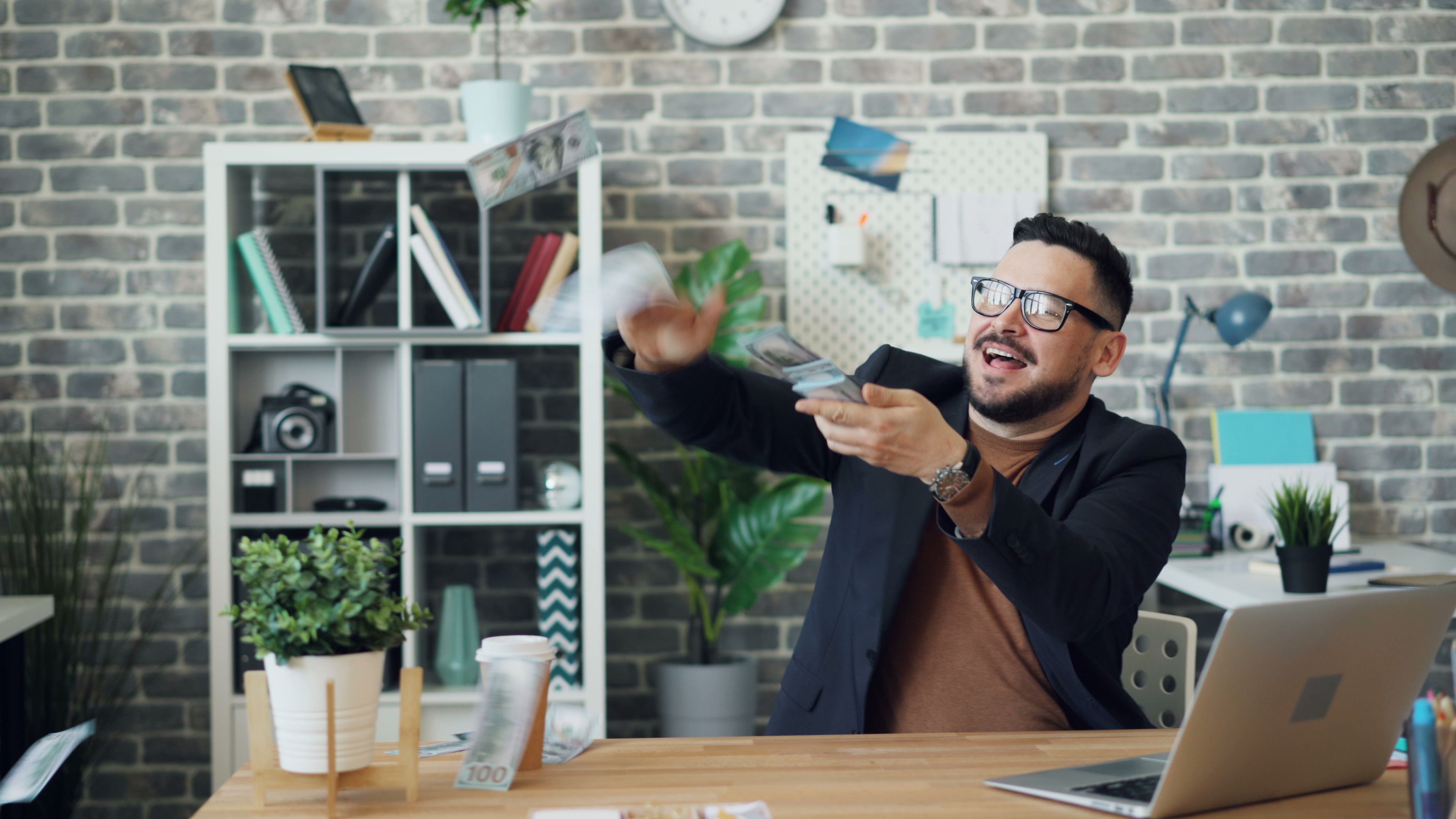 A Man Sitting at a Desk in an Office and Throwing Money · Free Stock Photo