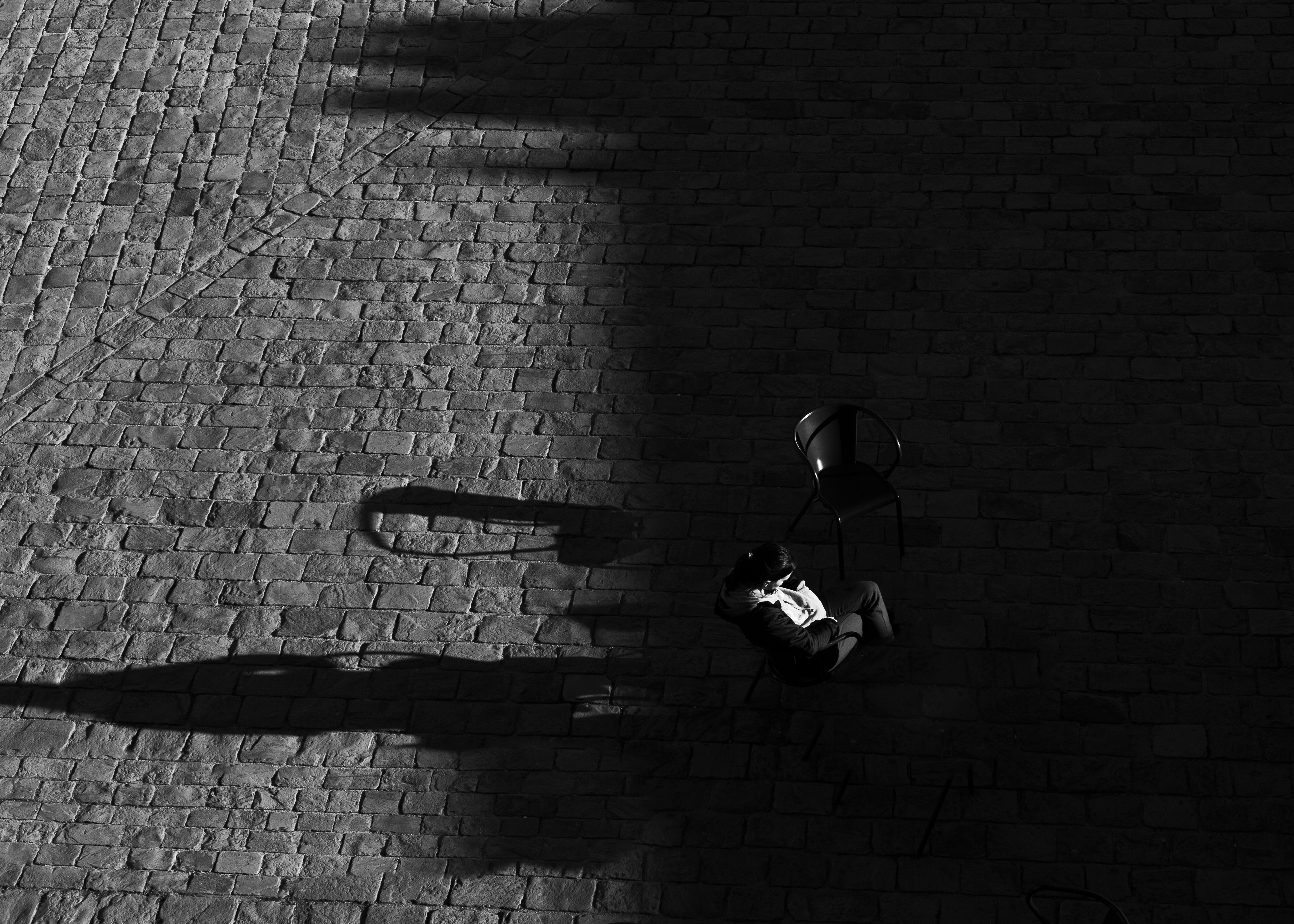 Person Sitting on Chair on Pavement in Shadow · Free Stock Photo