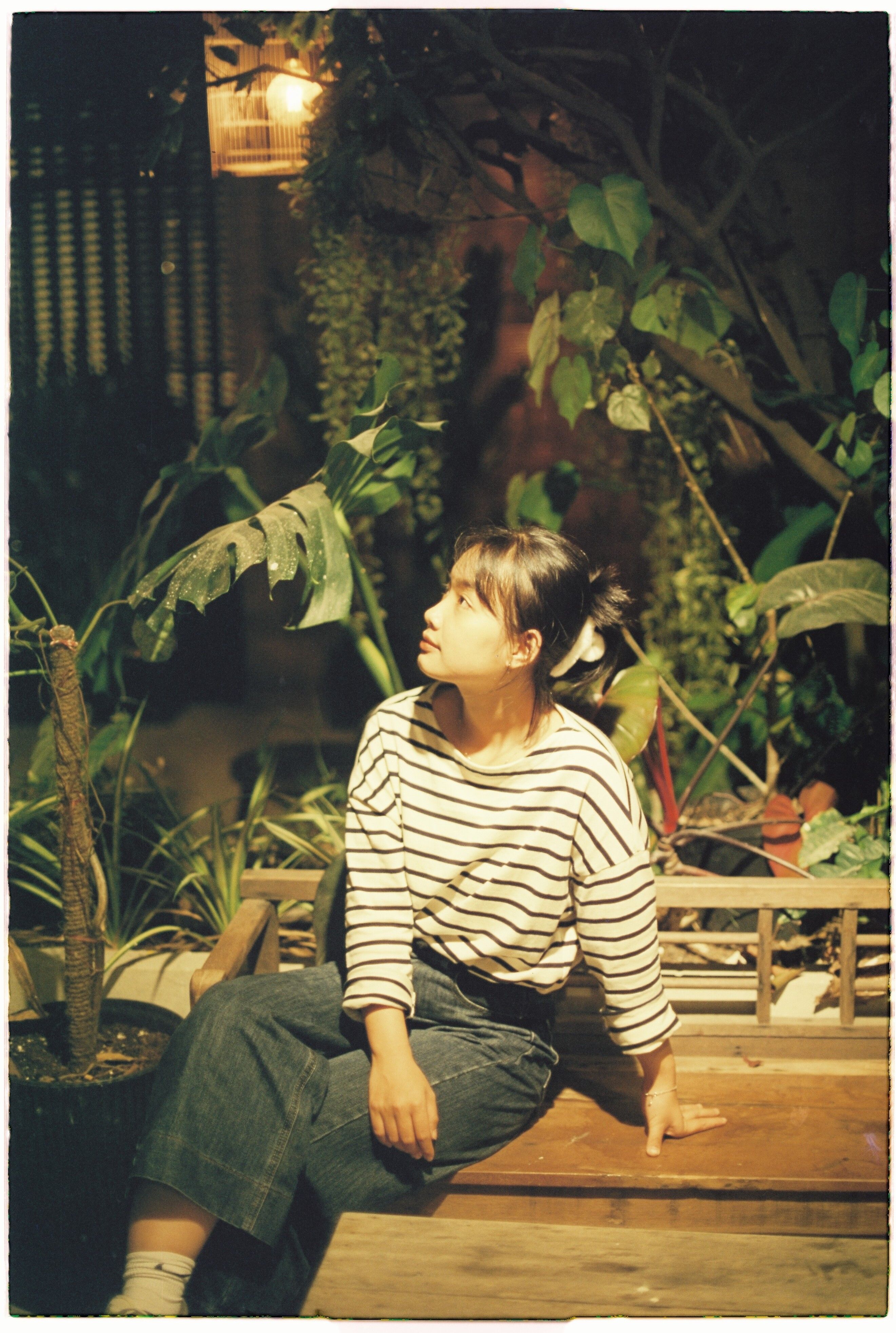 Young Woman Sitting on a Bench among Potted Plants and Looking up ...