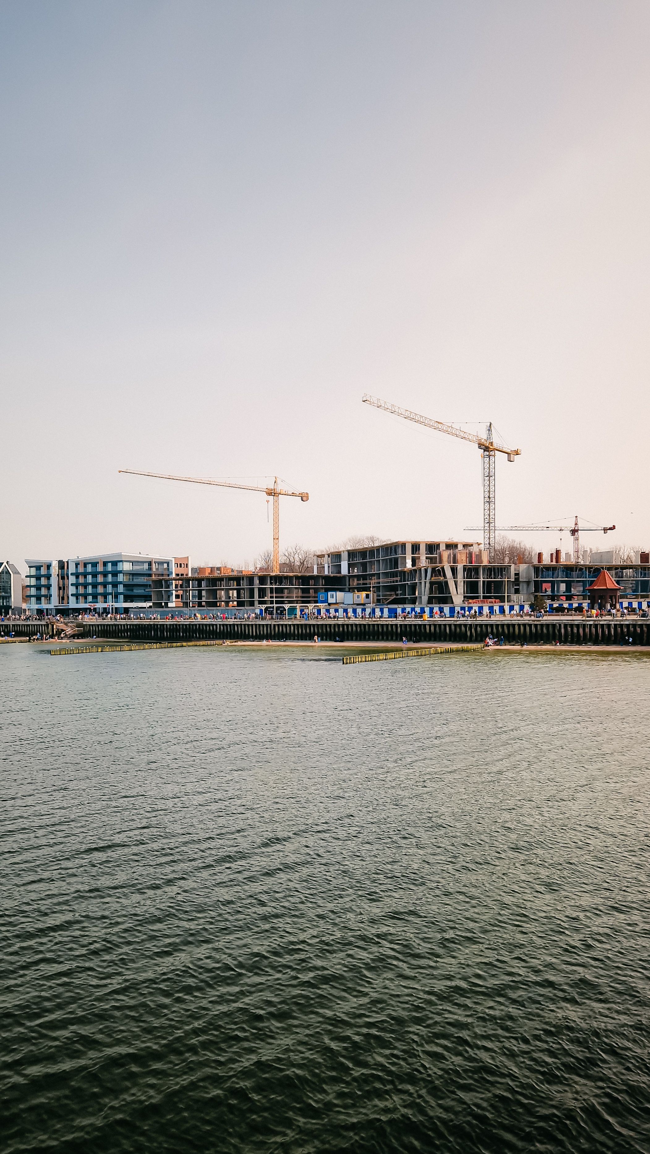 Construction cranes are seen over the water · Free Stock Photo