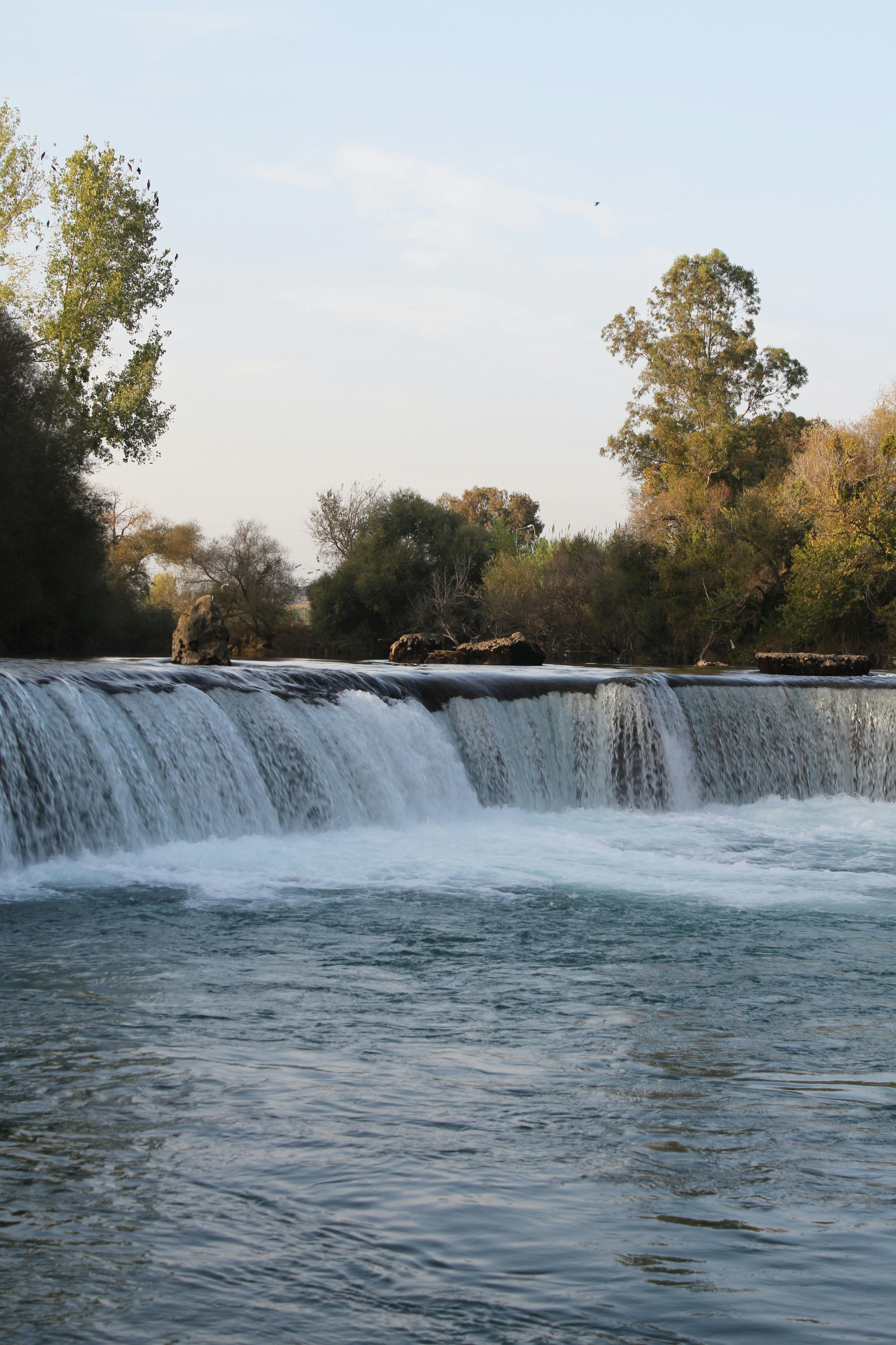 A waterfall is flowing over a river · Free Stock Photo