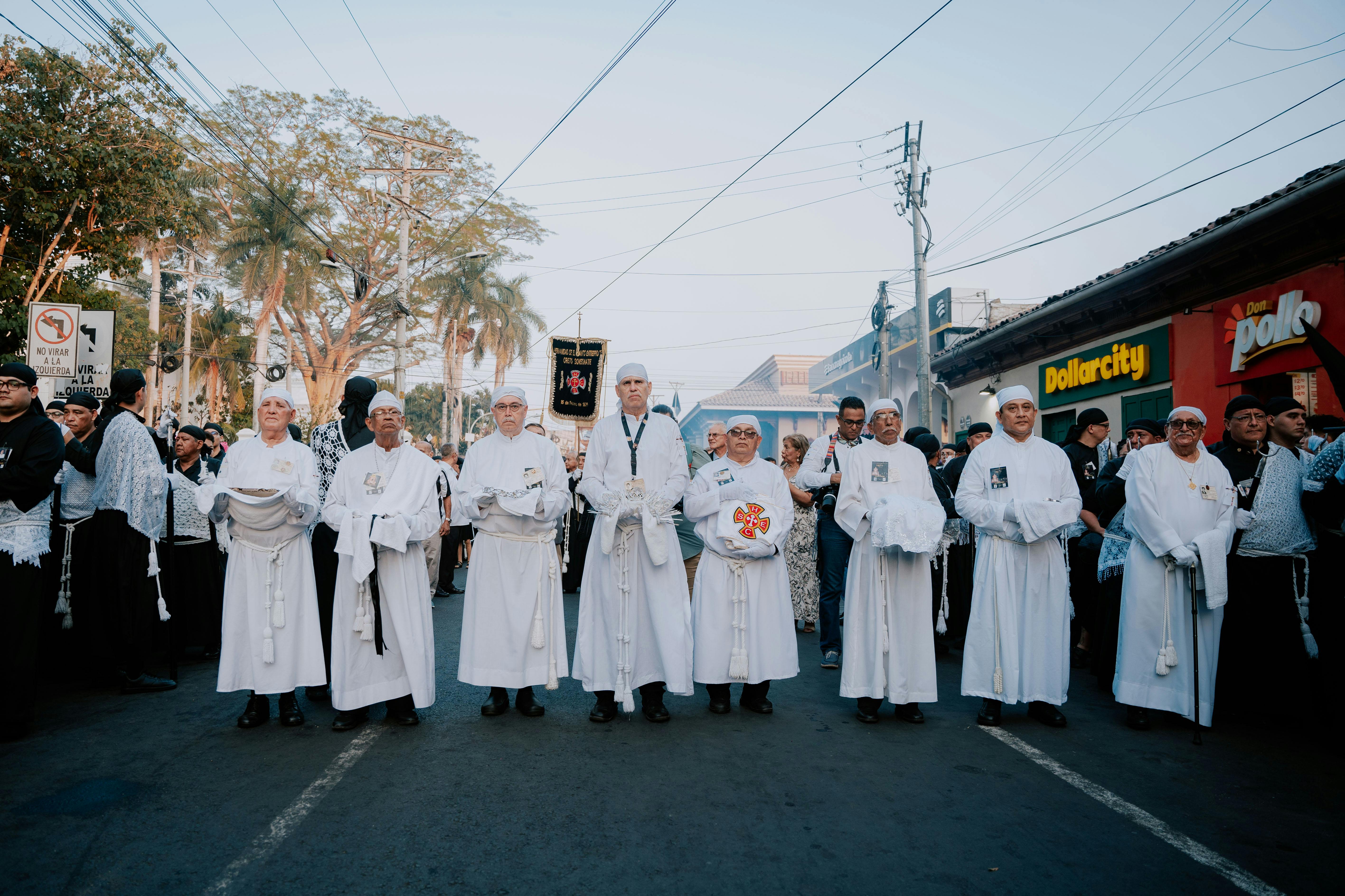 A group of priests in white robes walking down a street · Free Stock Photo