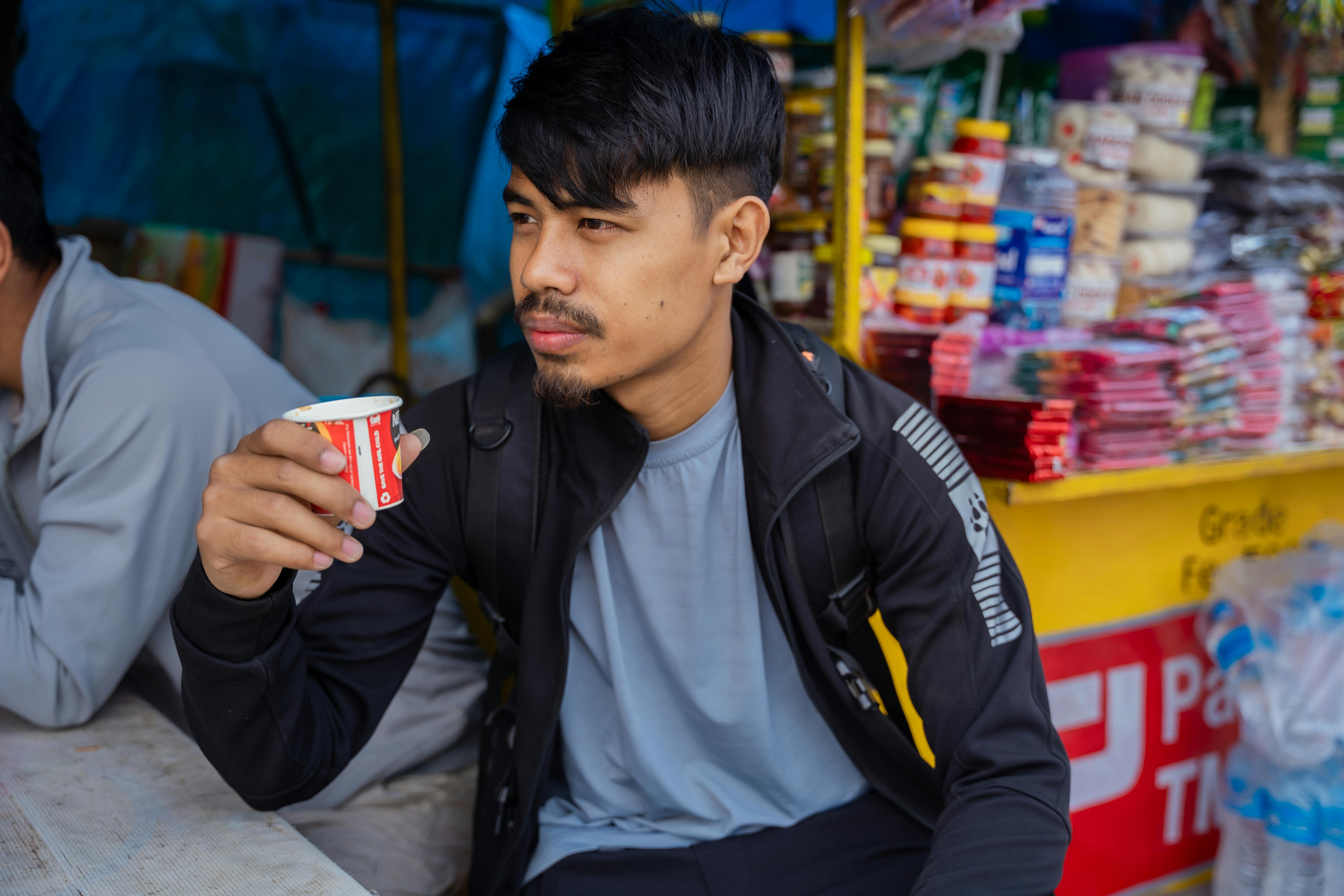 Man Drinking from a Paper Cup by a Kiosk · Free Stock Photo