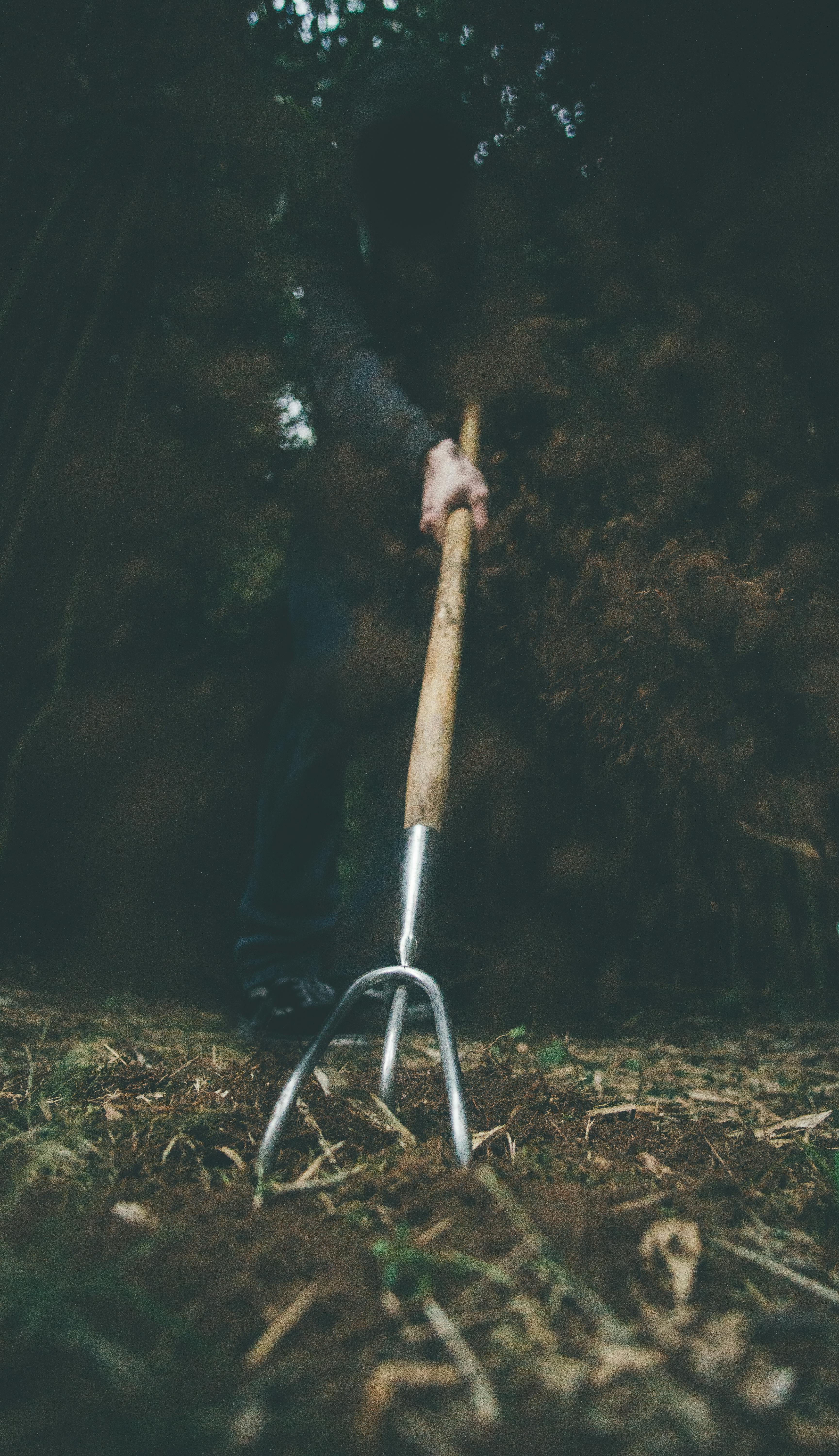 Black-clad Hooded Figure Raking Soil in the Forest · Free Stock Photo