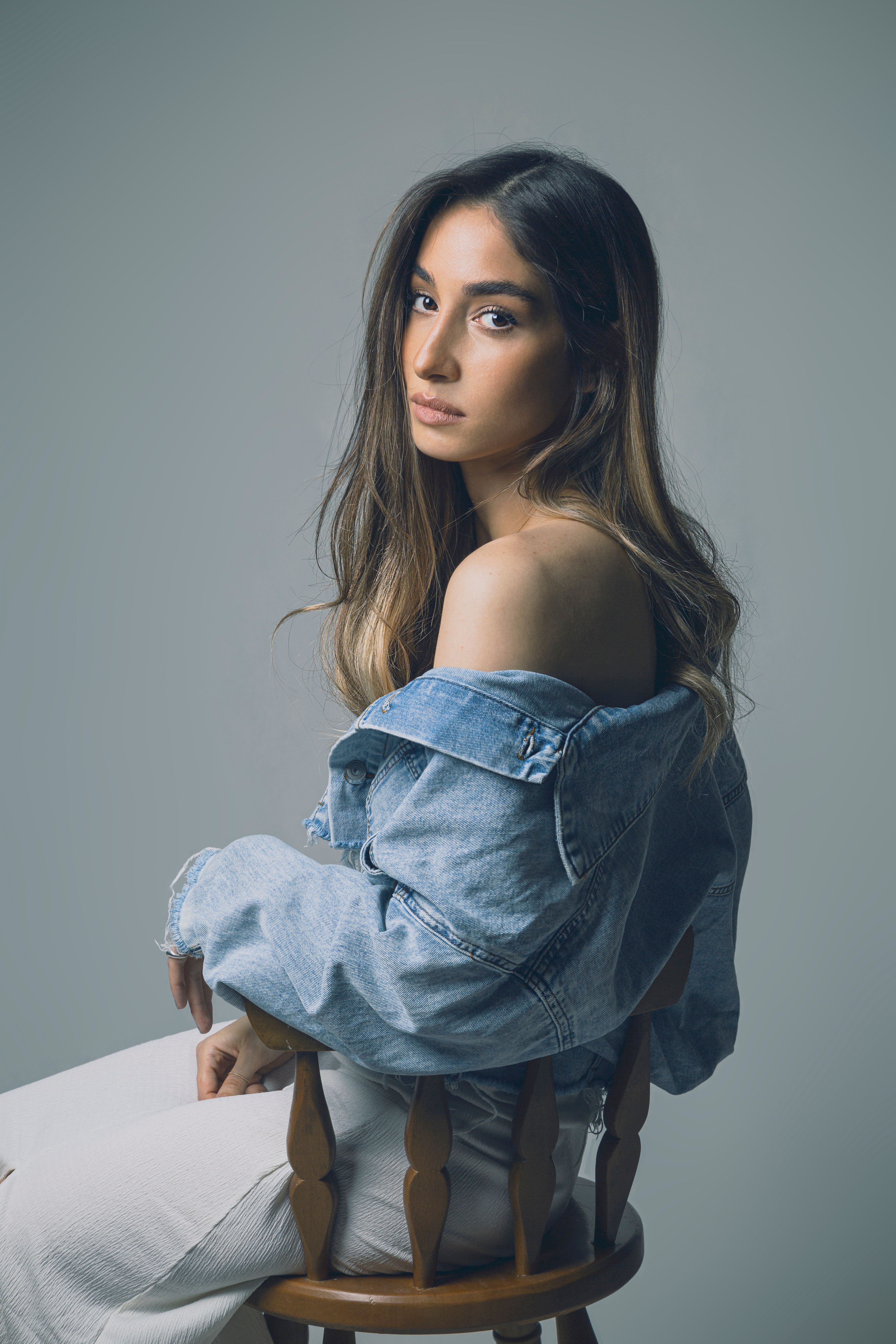 Studio Shot of a Young Woman Wearing a Denim Jacket Sitting on a Chair ...