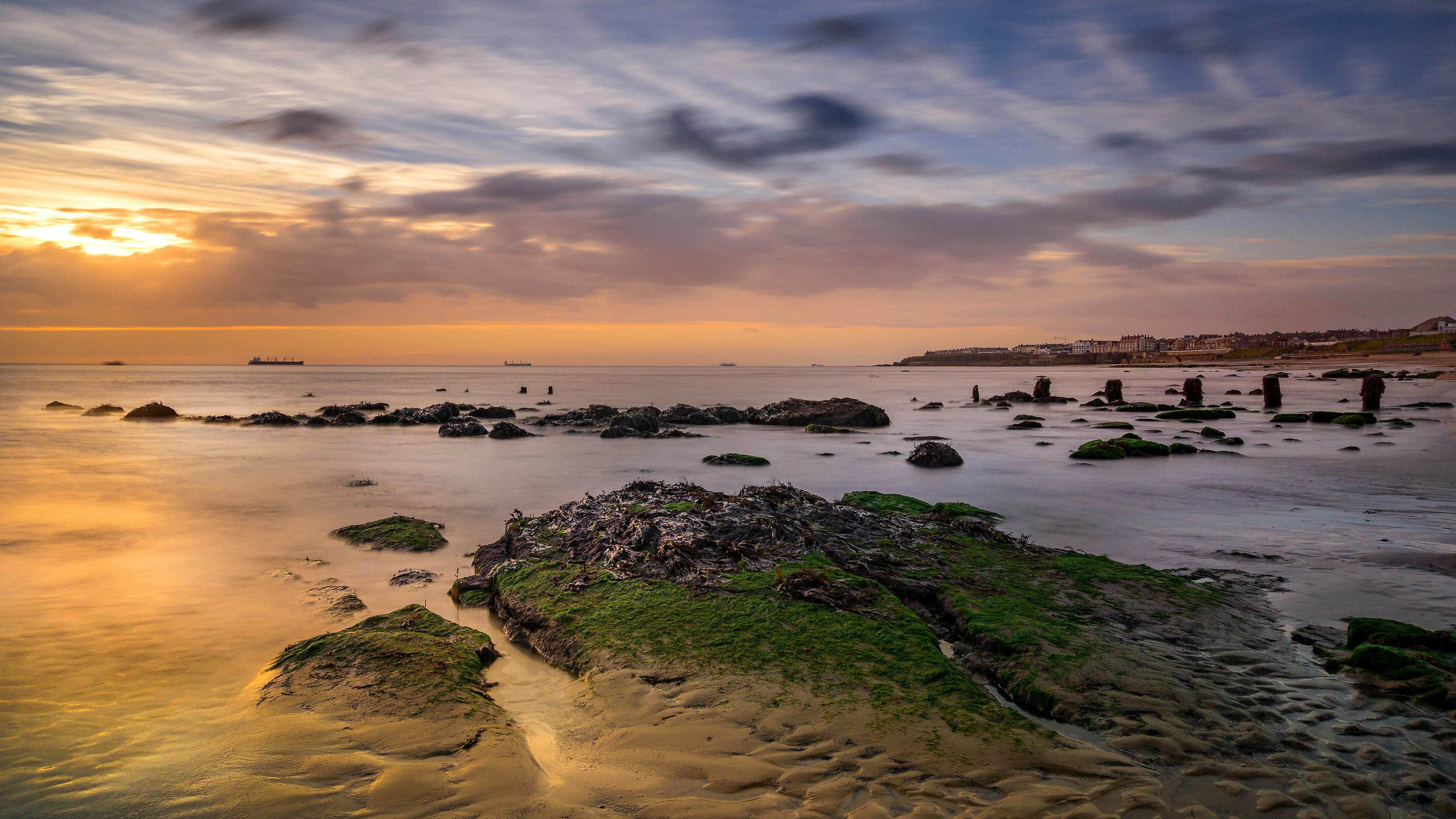 A sunset over the ocean with rocks and sand · Free Stock Photo