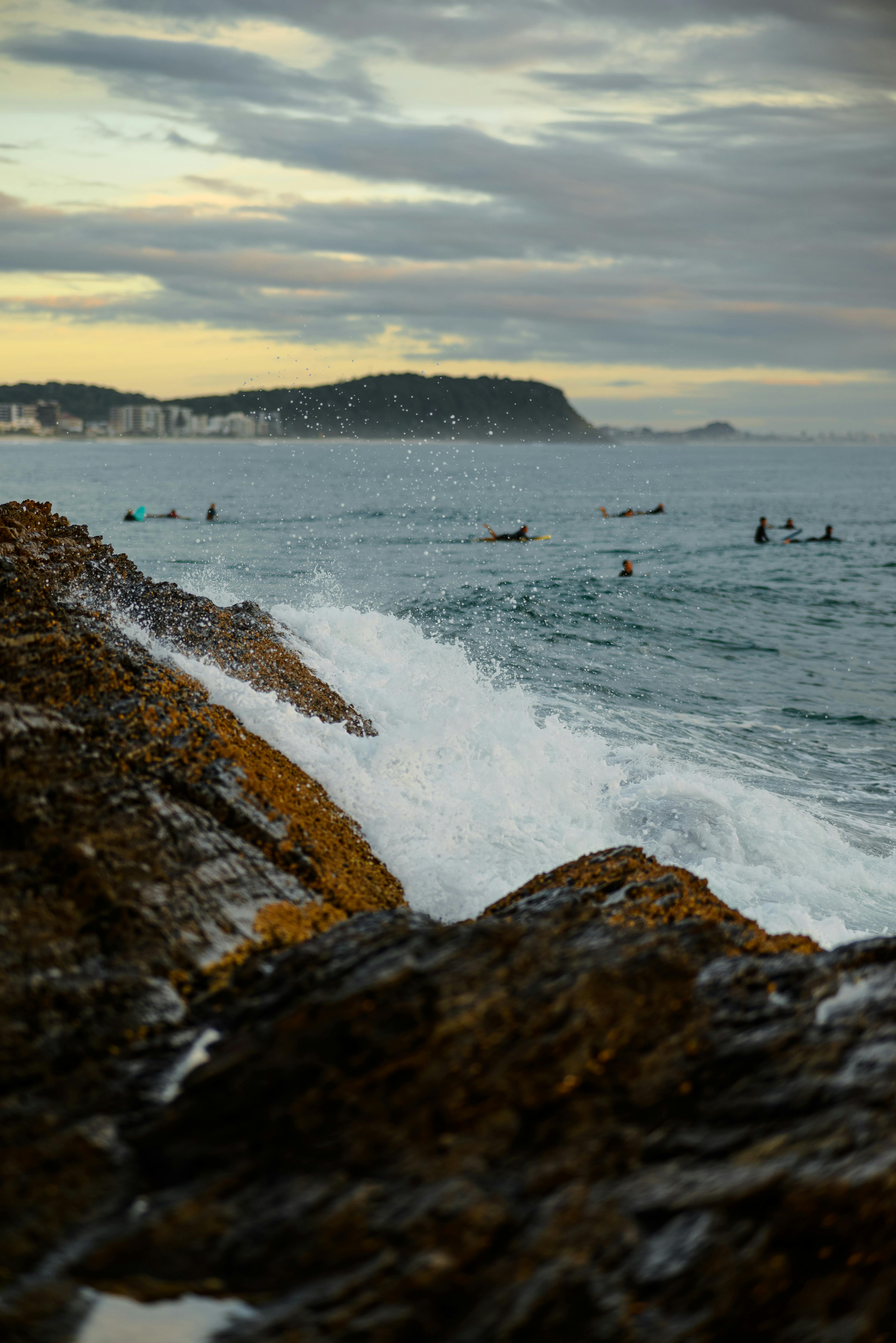Rocks and Surfers on Sea Shore at Sunset · Free Stock Photo
