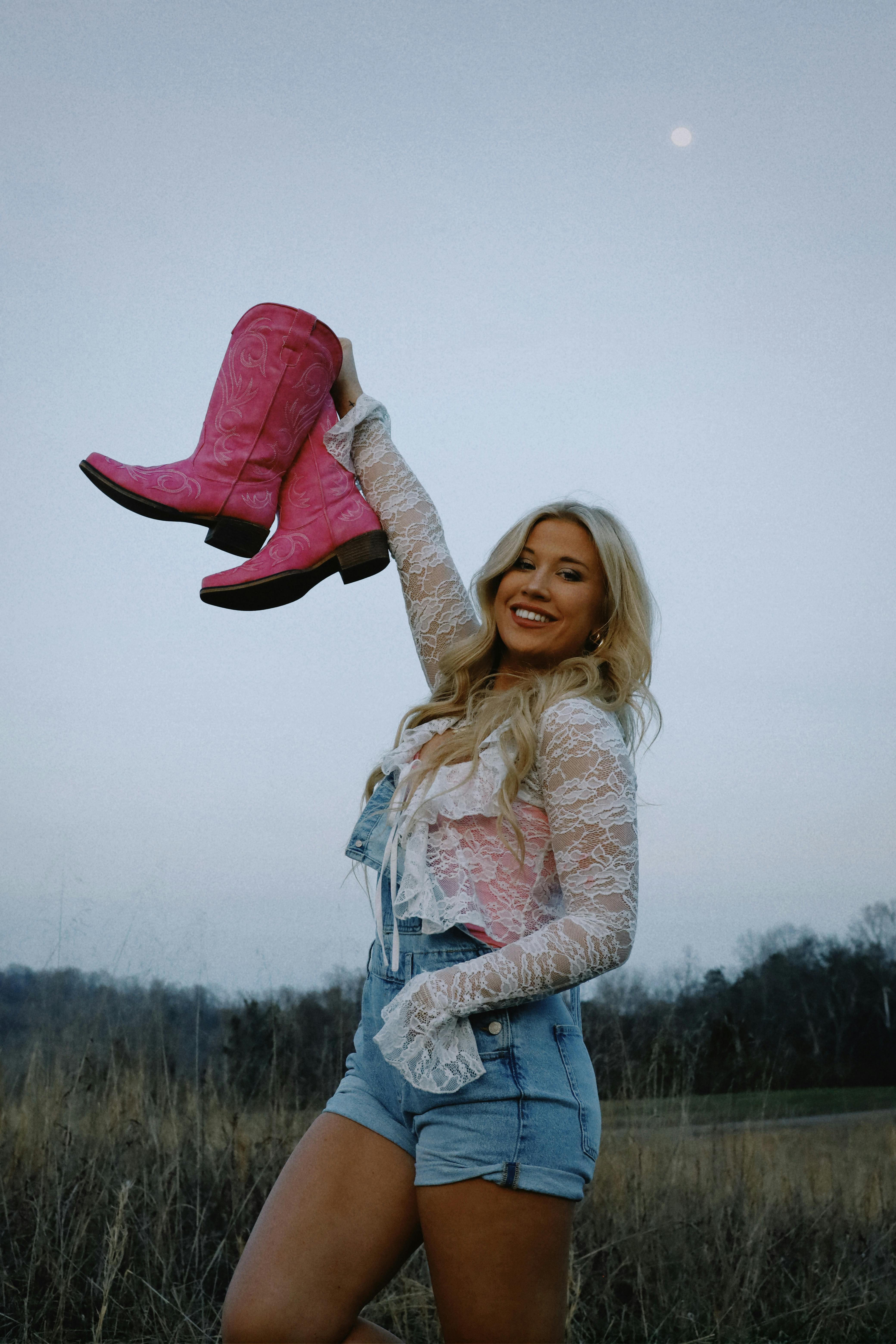 Smiling Blonde Woman Holding Boots in Raised Arm · Free Stock Photo