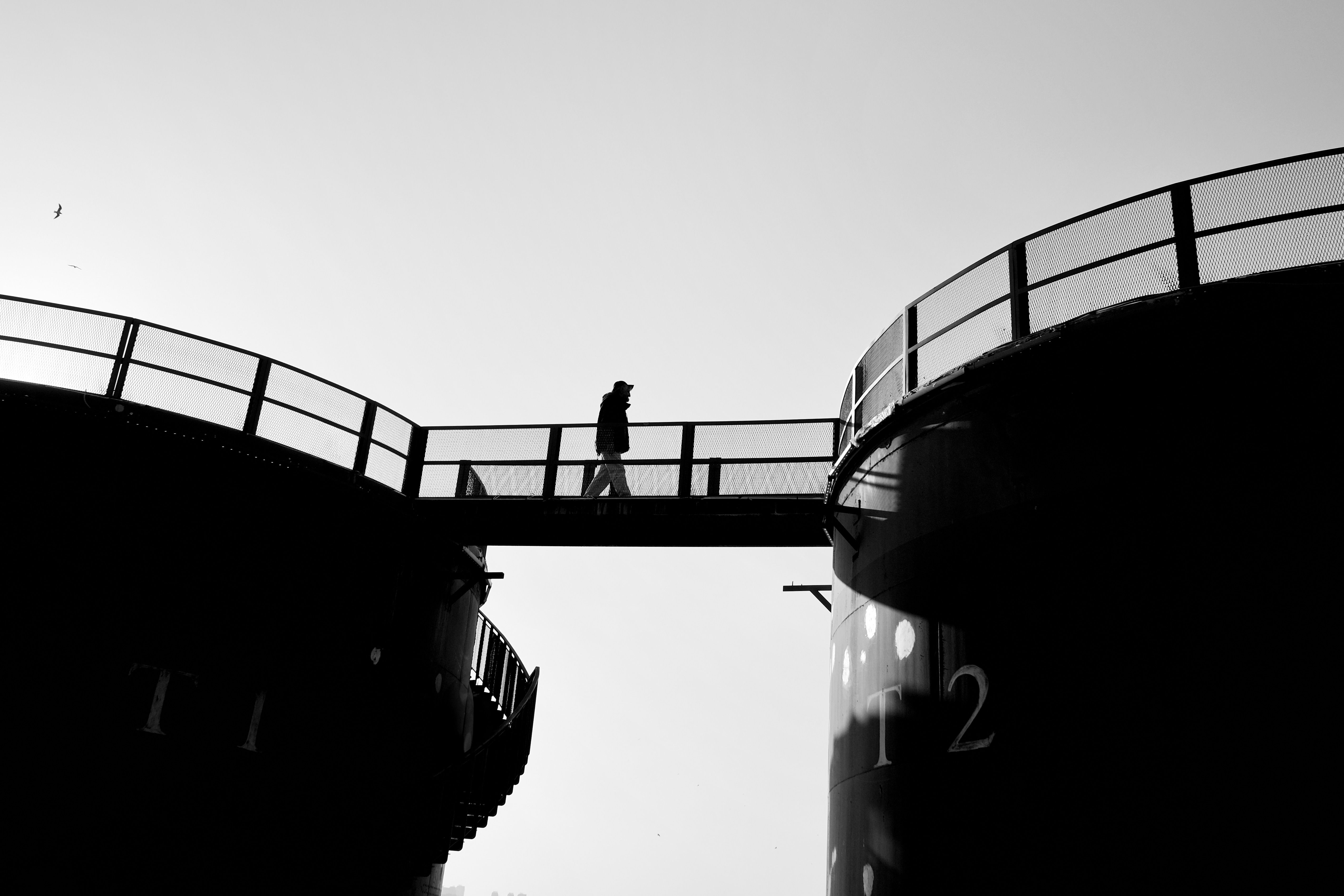 Man Walking on Footbridge between Silos · Free Stock Photo