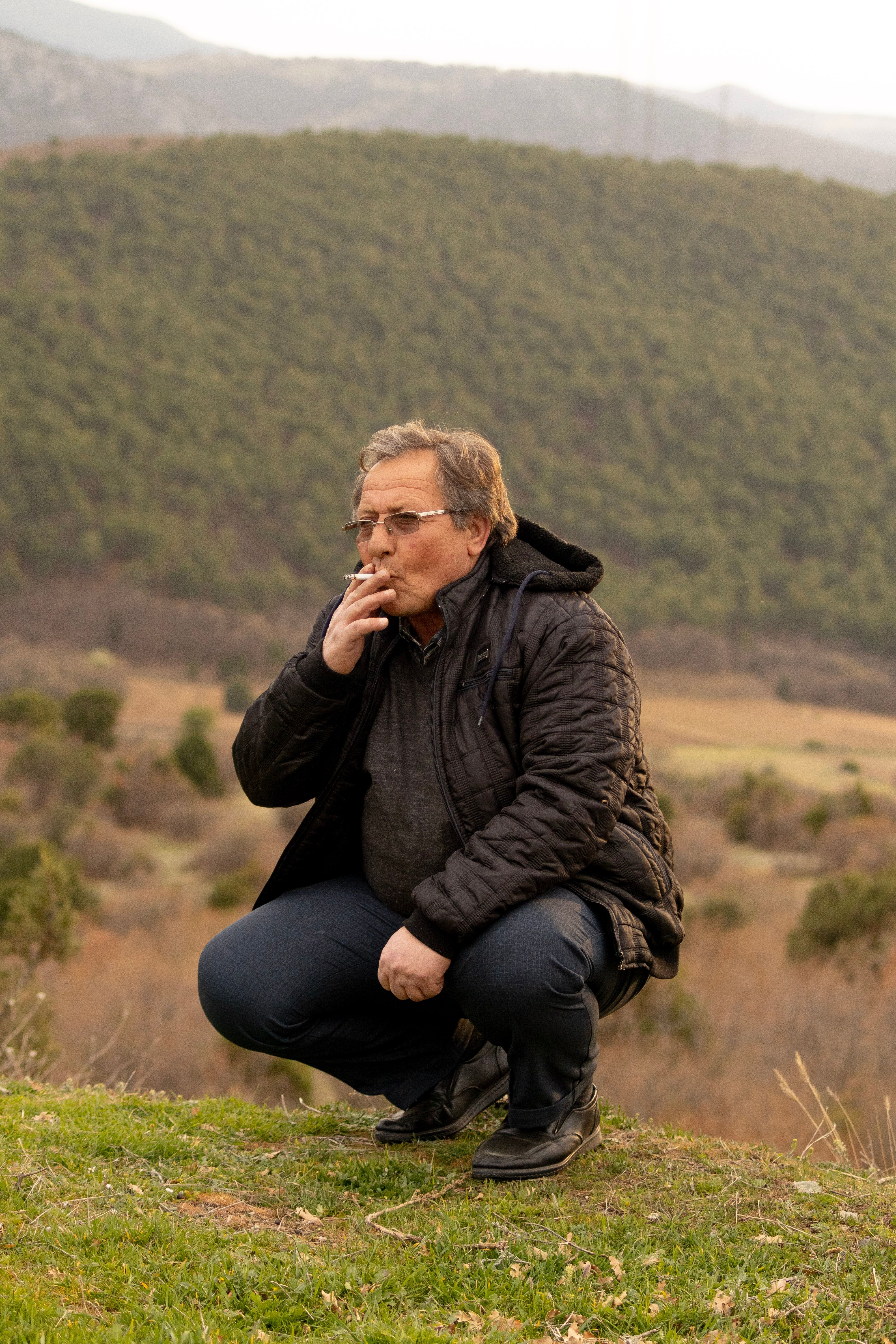 Man in Jacket Squatting and Smoking Cigarette · Free Stock Photo