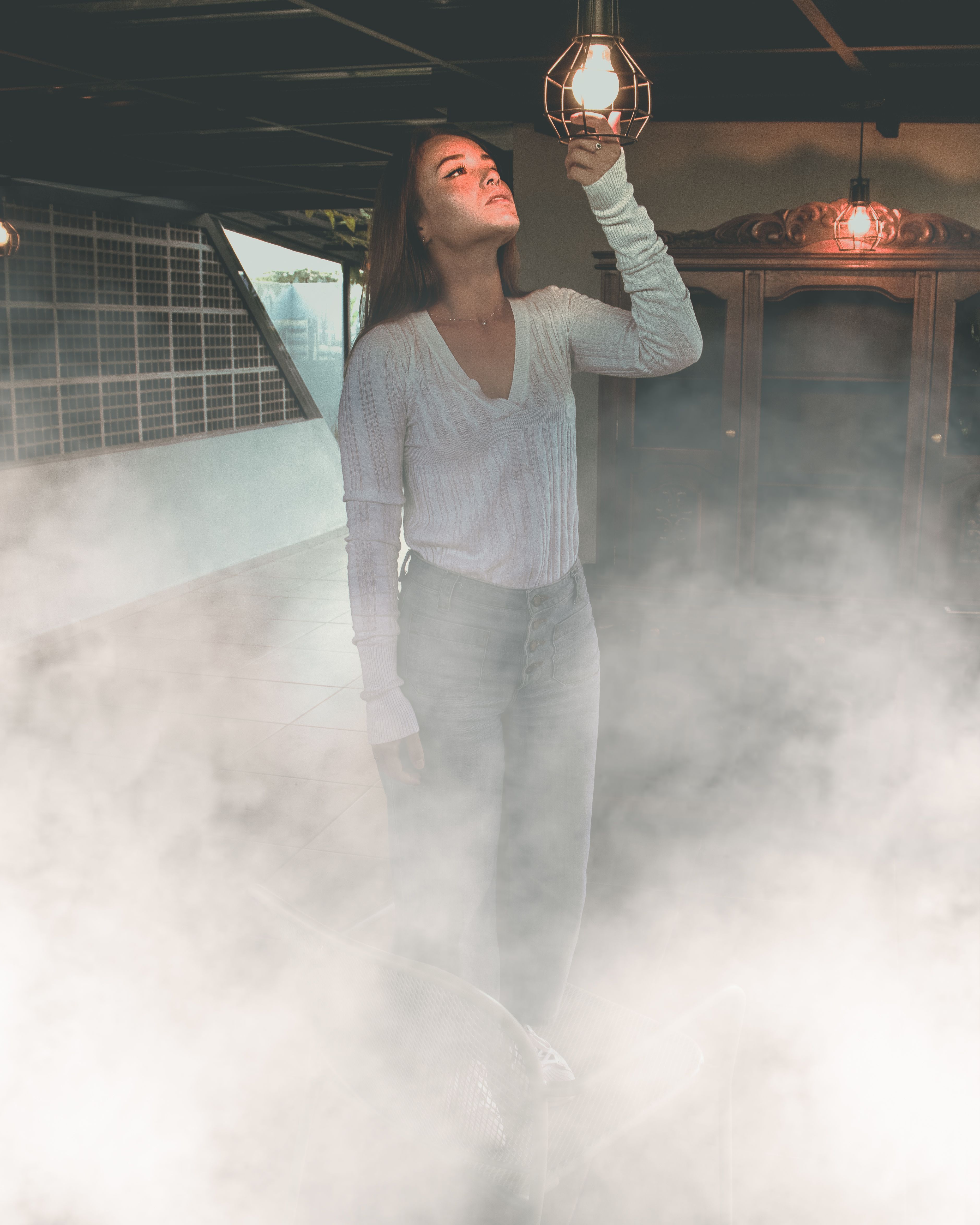 Woman Standing Inside Smoky Room and Holding Turned on Hanging Light ...