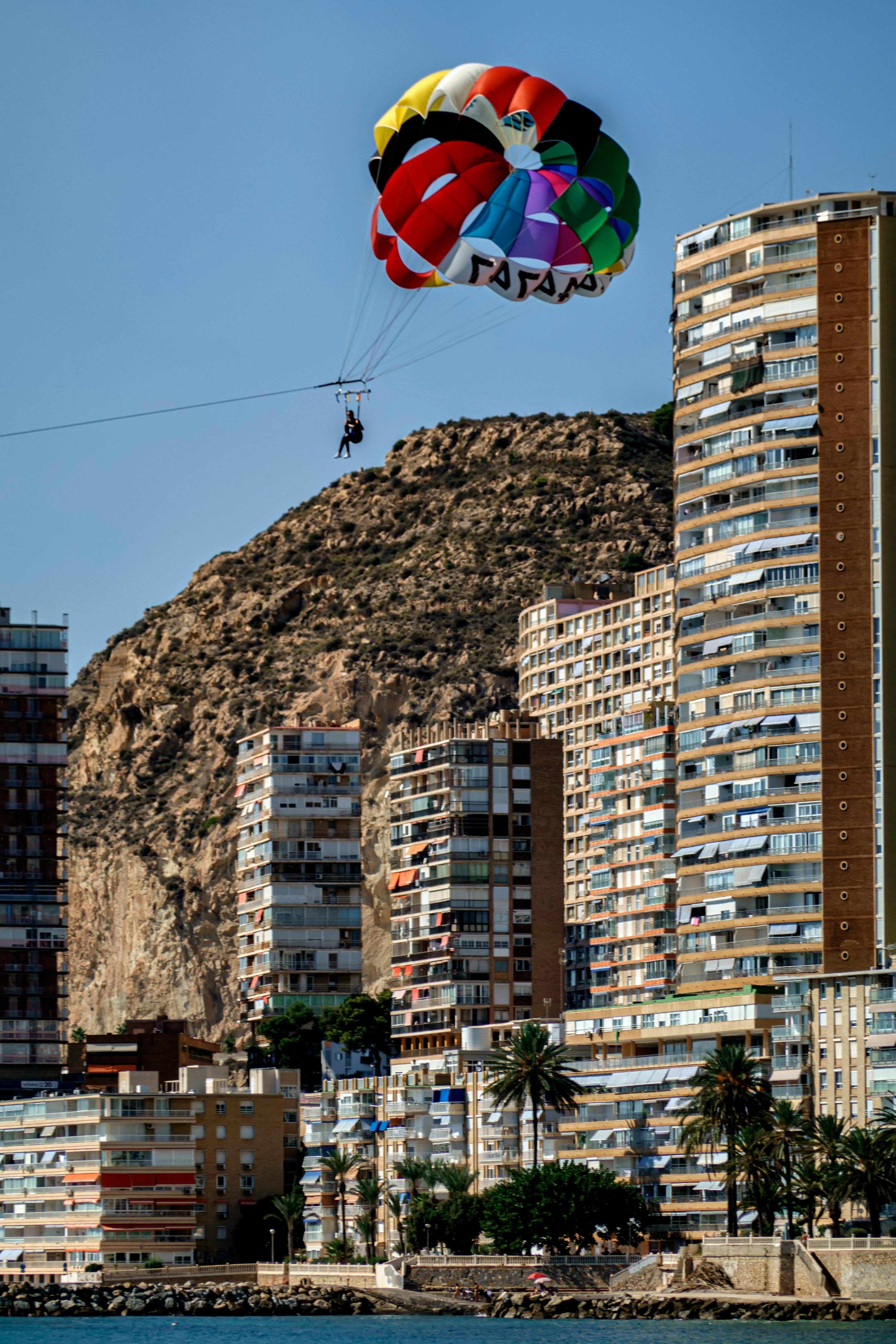 Colorful Parachute Over Tall Buildings by a Seashore · Free Stock Photo