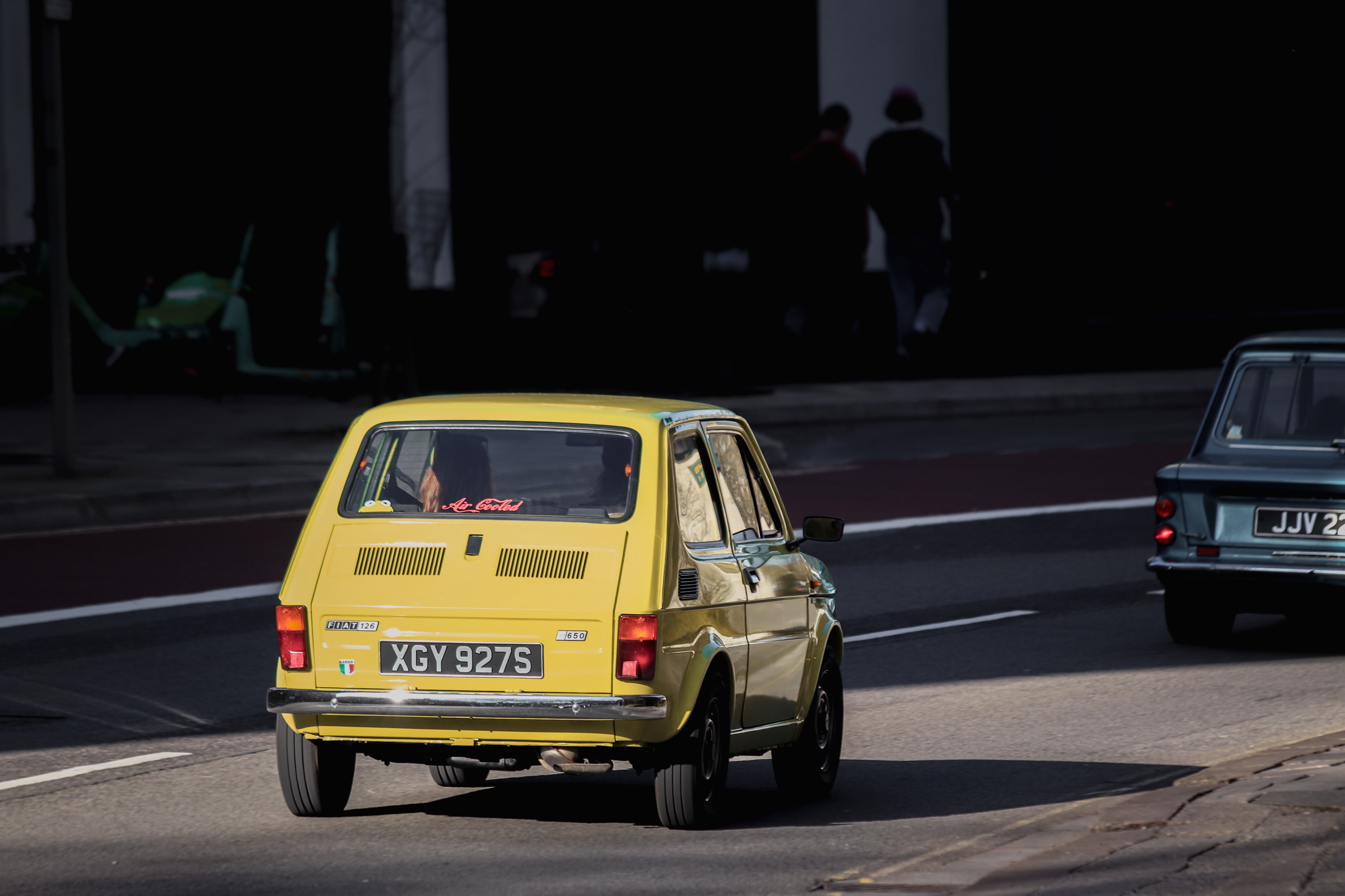 A small yellow car driving down the street · Free Stock Photo