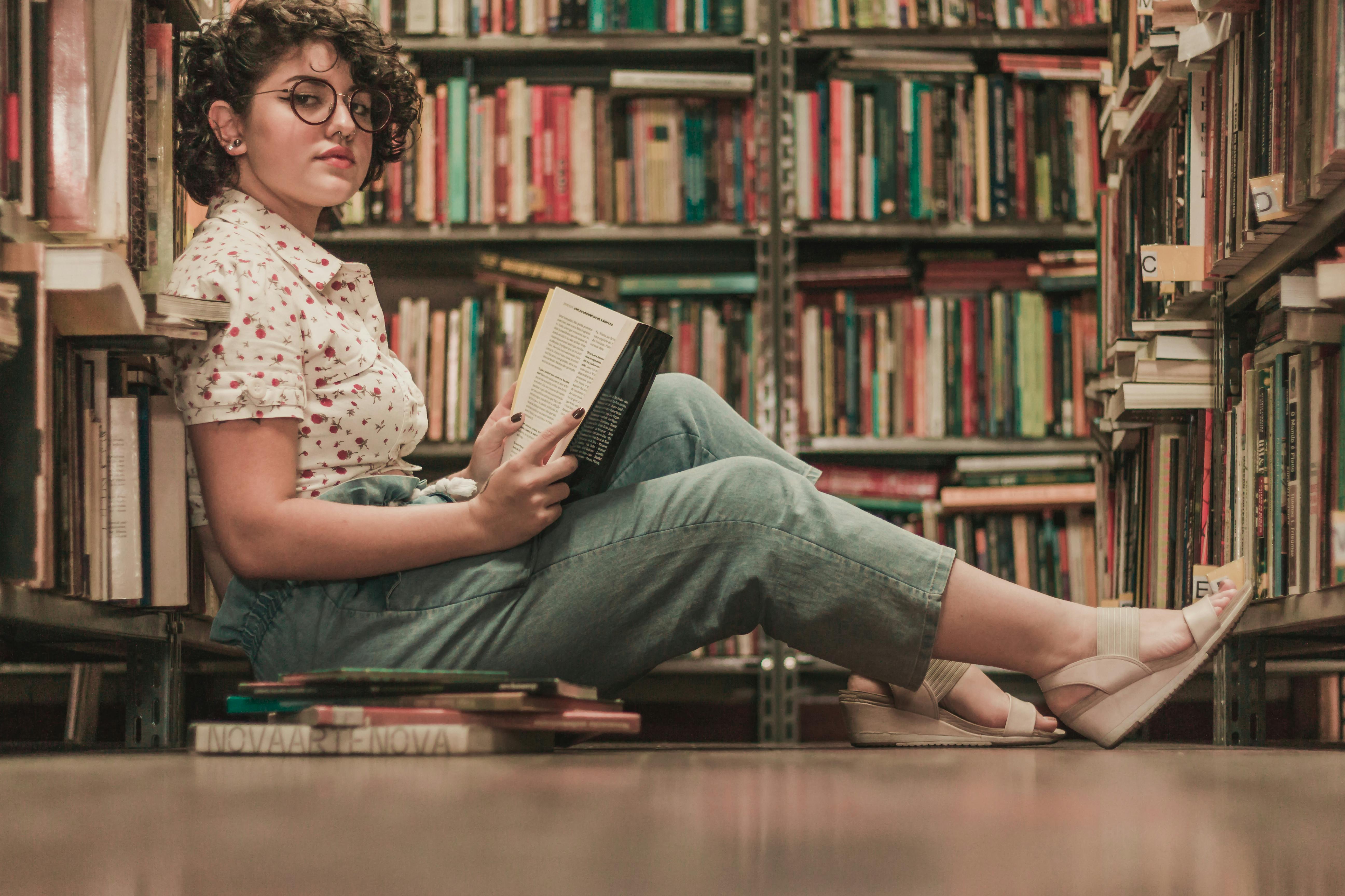 Woman Sits on the Floor Inside Library · Free Stock Photo