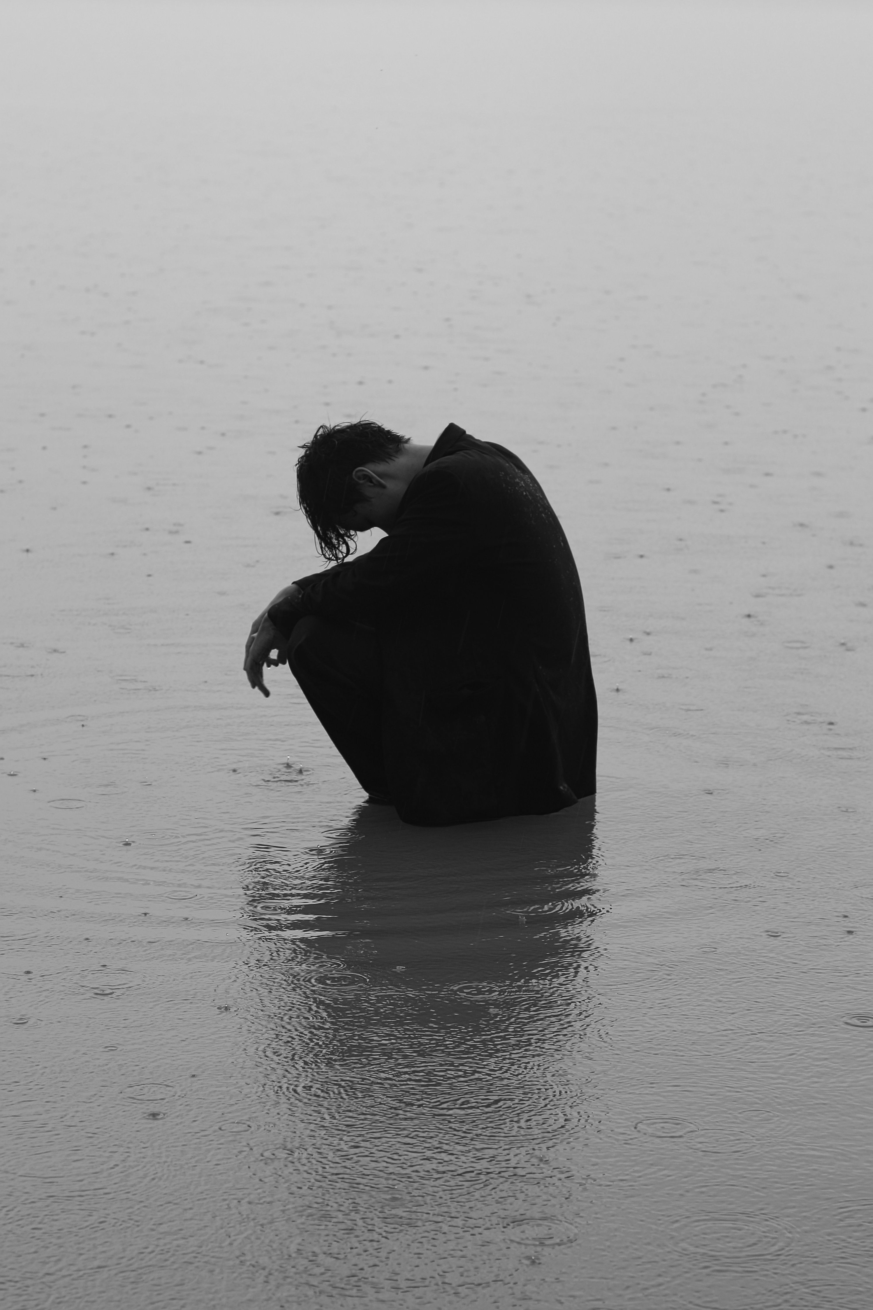 Man in Suit Sitting in Shallow Water During Rain · Free Stock Photo