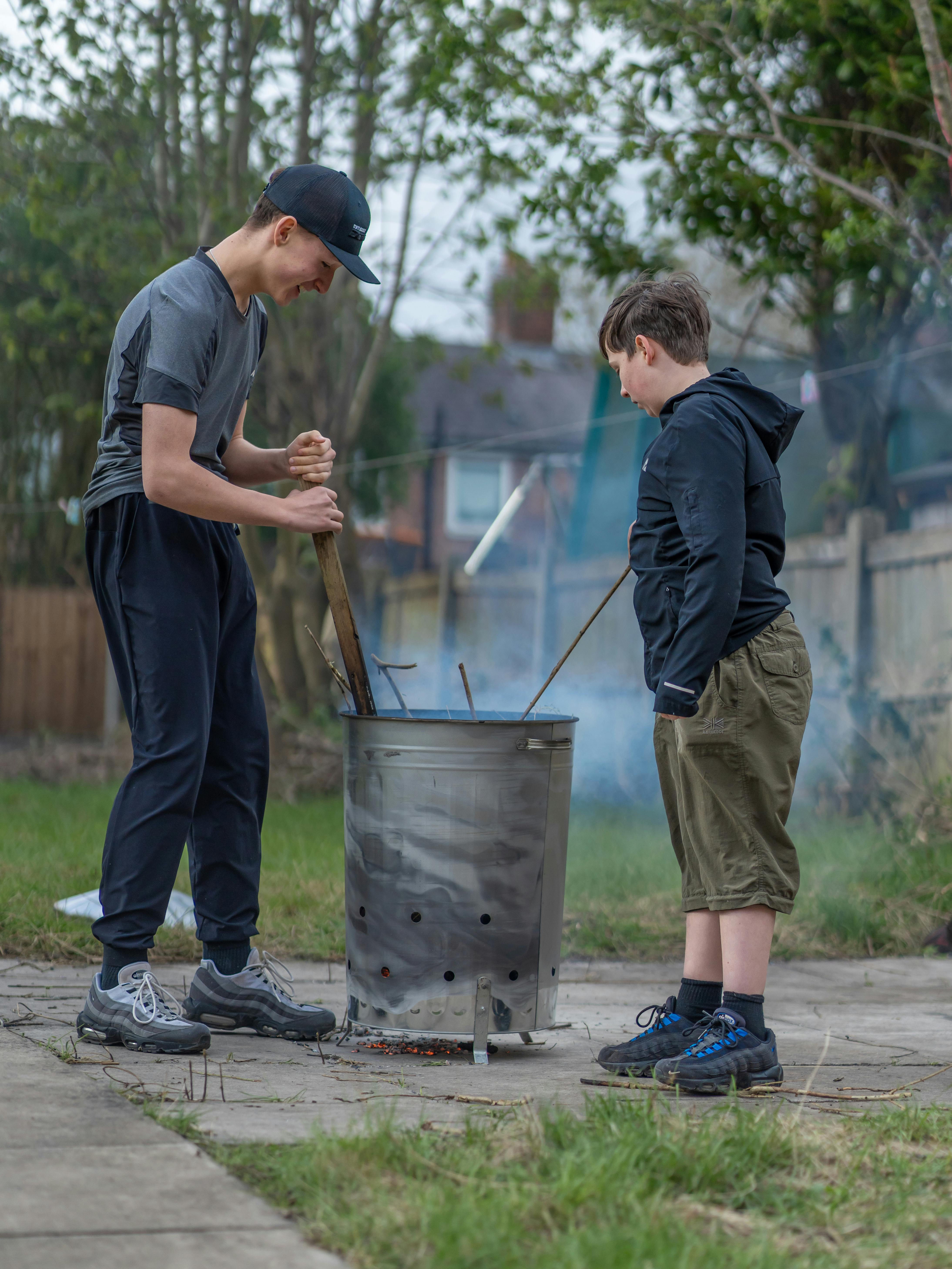 Two Boys Standing next to a Barrel with Burning Sticks · Free Stock Photo