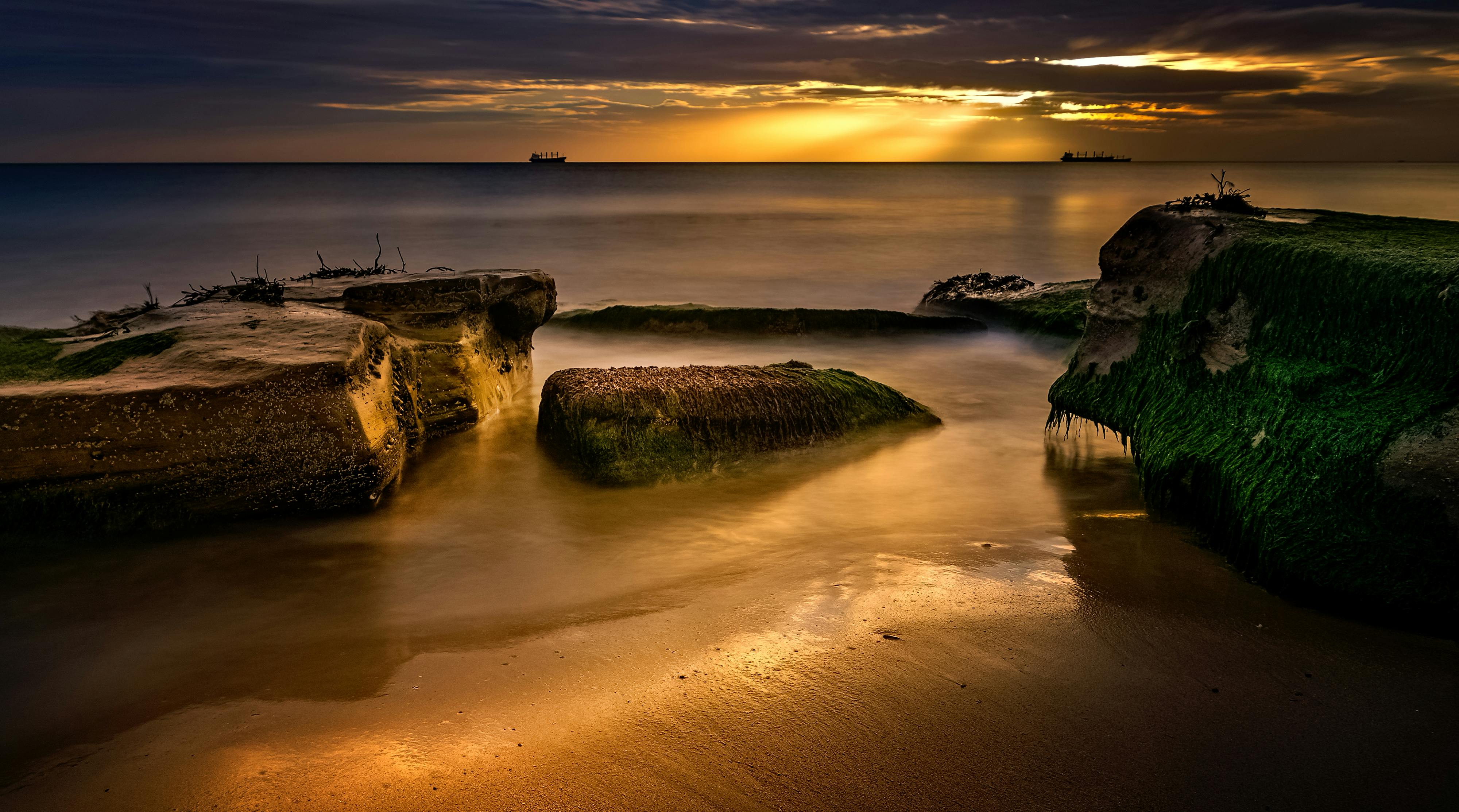A sunset over rocks and water at the beach · Free Stock Photo