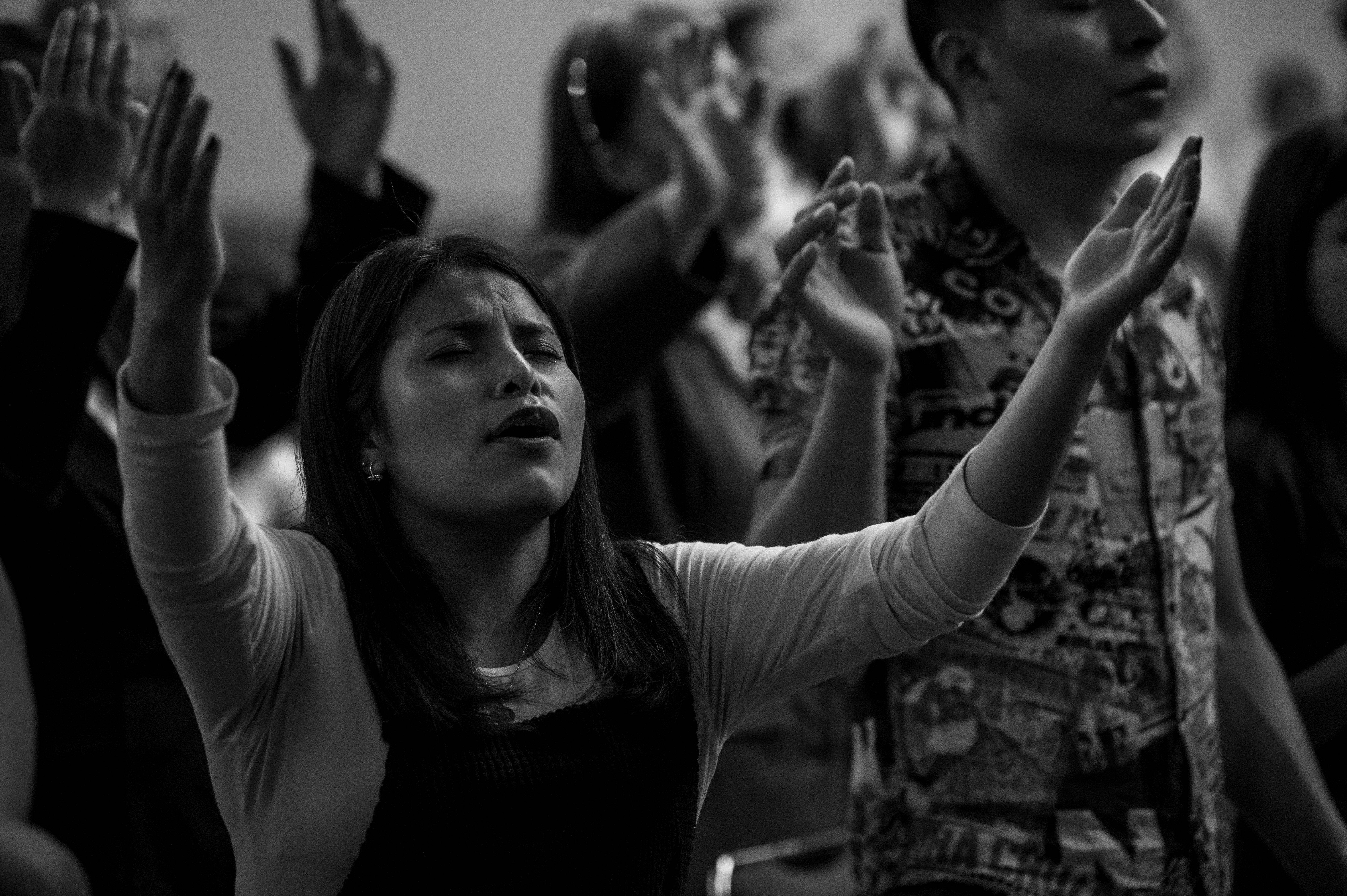 Woman Standing with Arms Raised and Praying at Gathering · Free Stock Photo