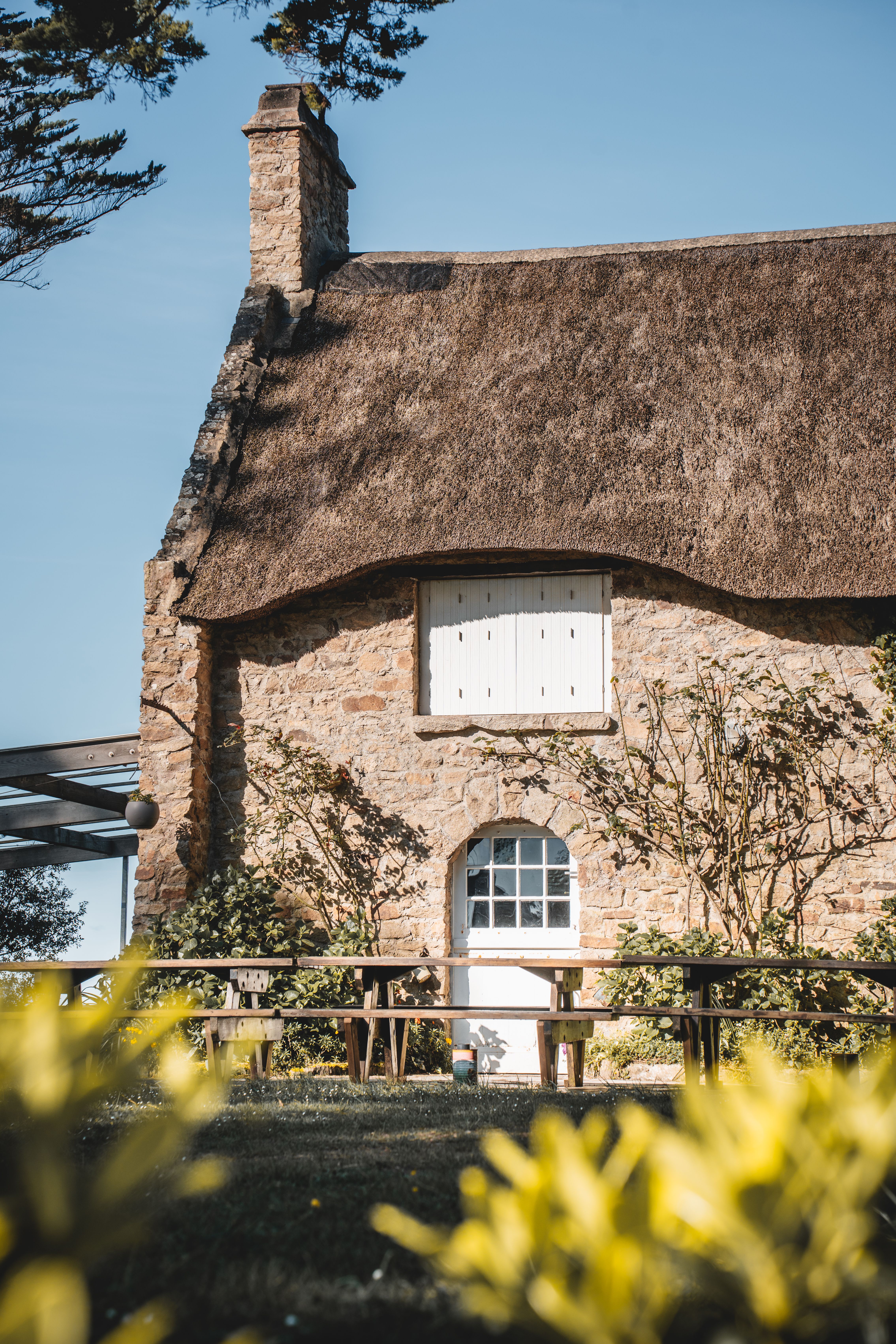 A thatched cottage with a bench and picnic table · Free Stock Photo