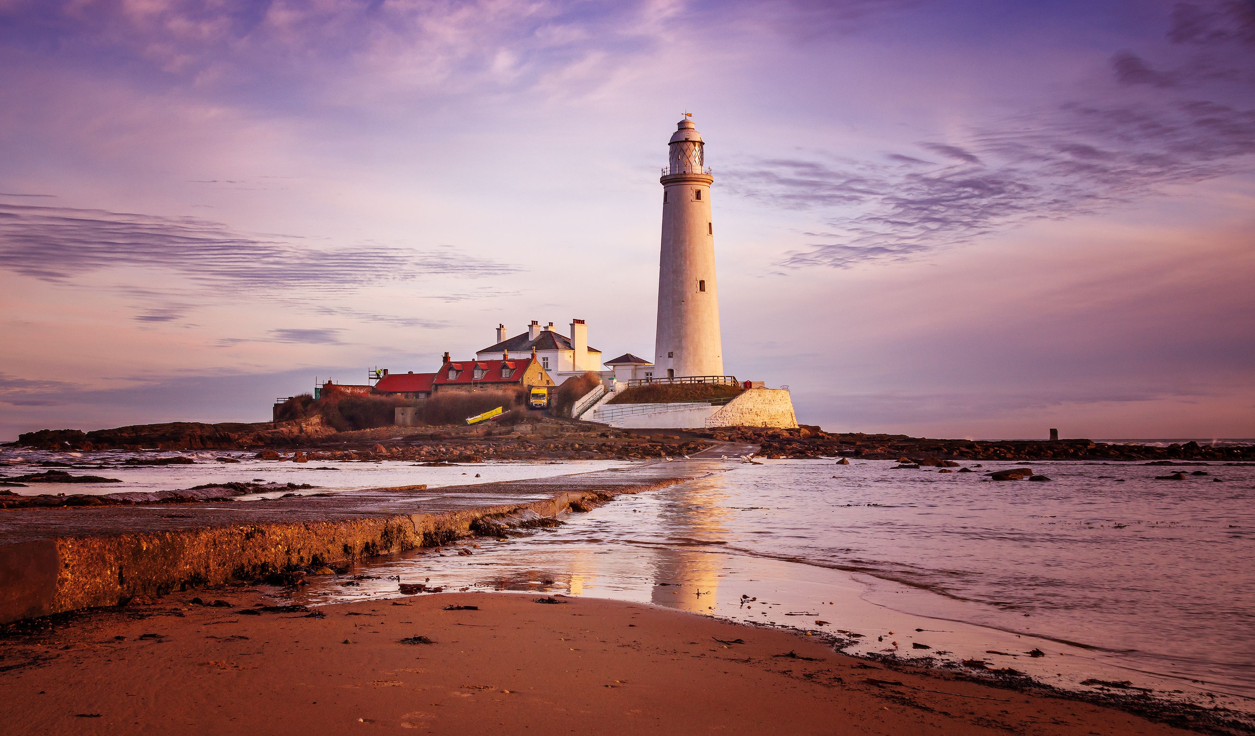 A lighthouse is on the beach at sunset · Free Stock Photo