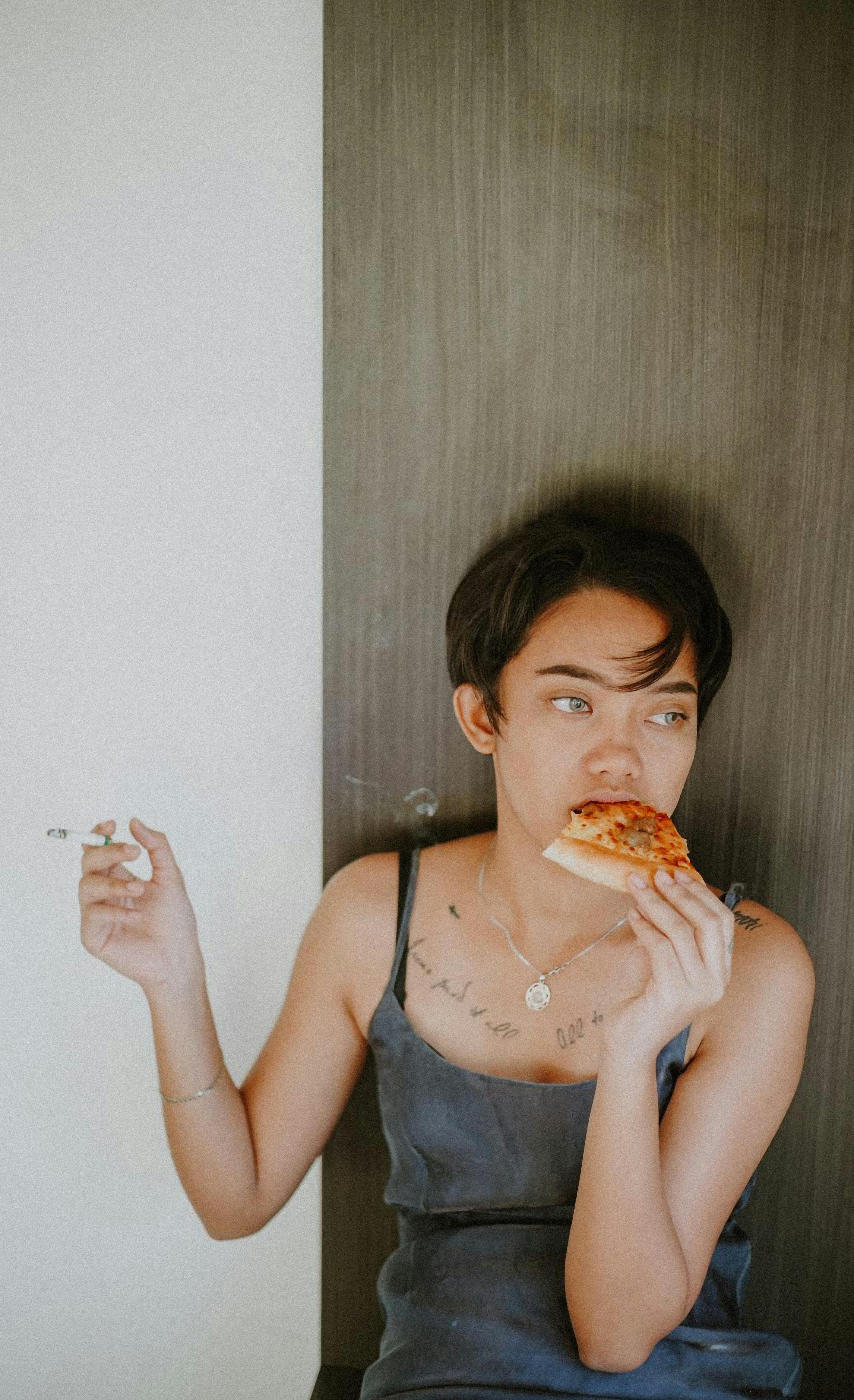 Young Woman Eating a Piece of Pizza and Smoking a Cigarette · Free ...