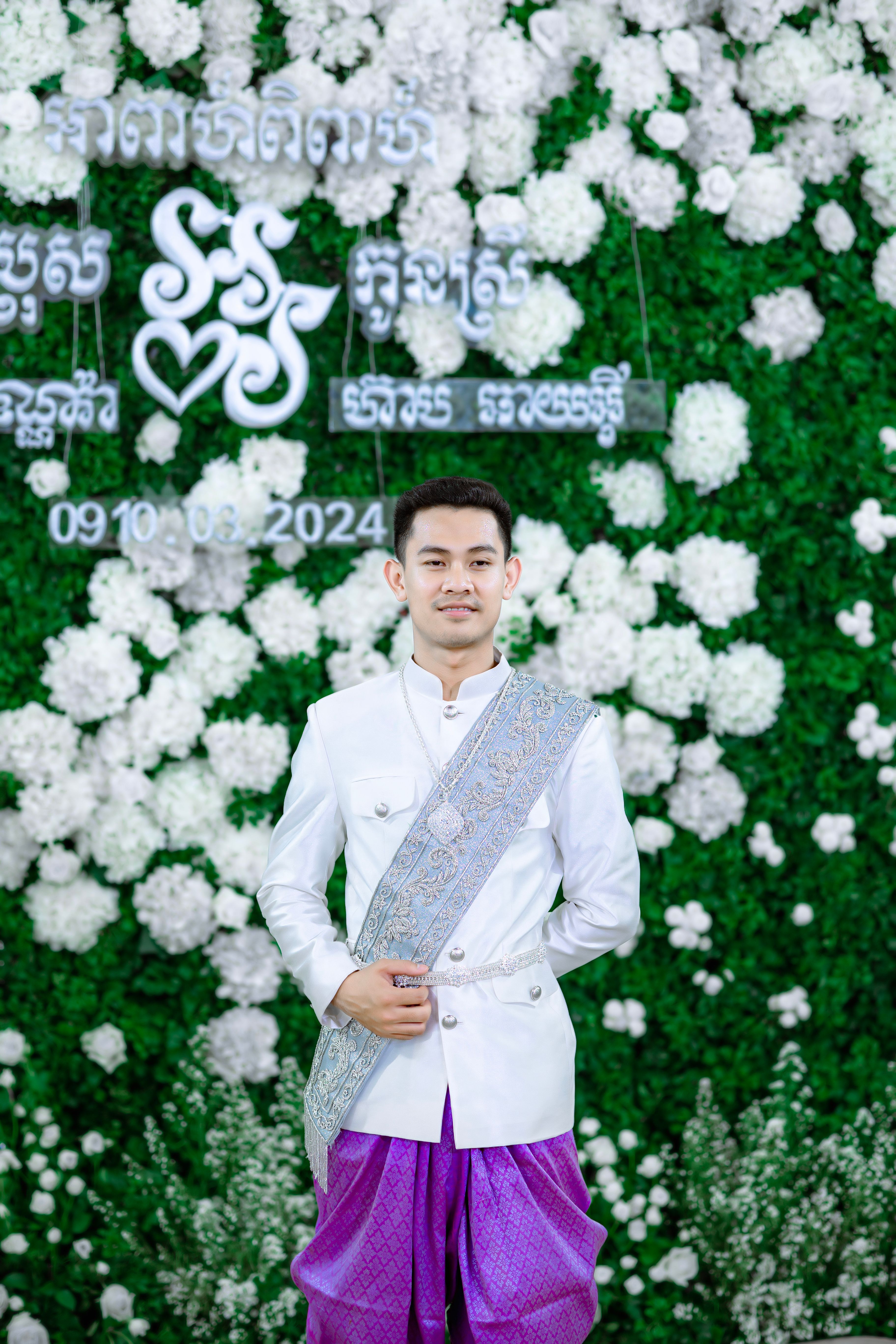 A man in a purple sash and white pants standing in front of a floral ...