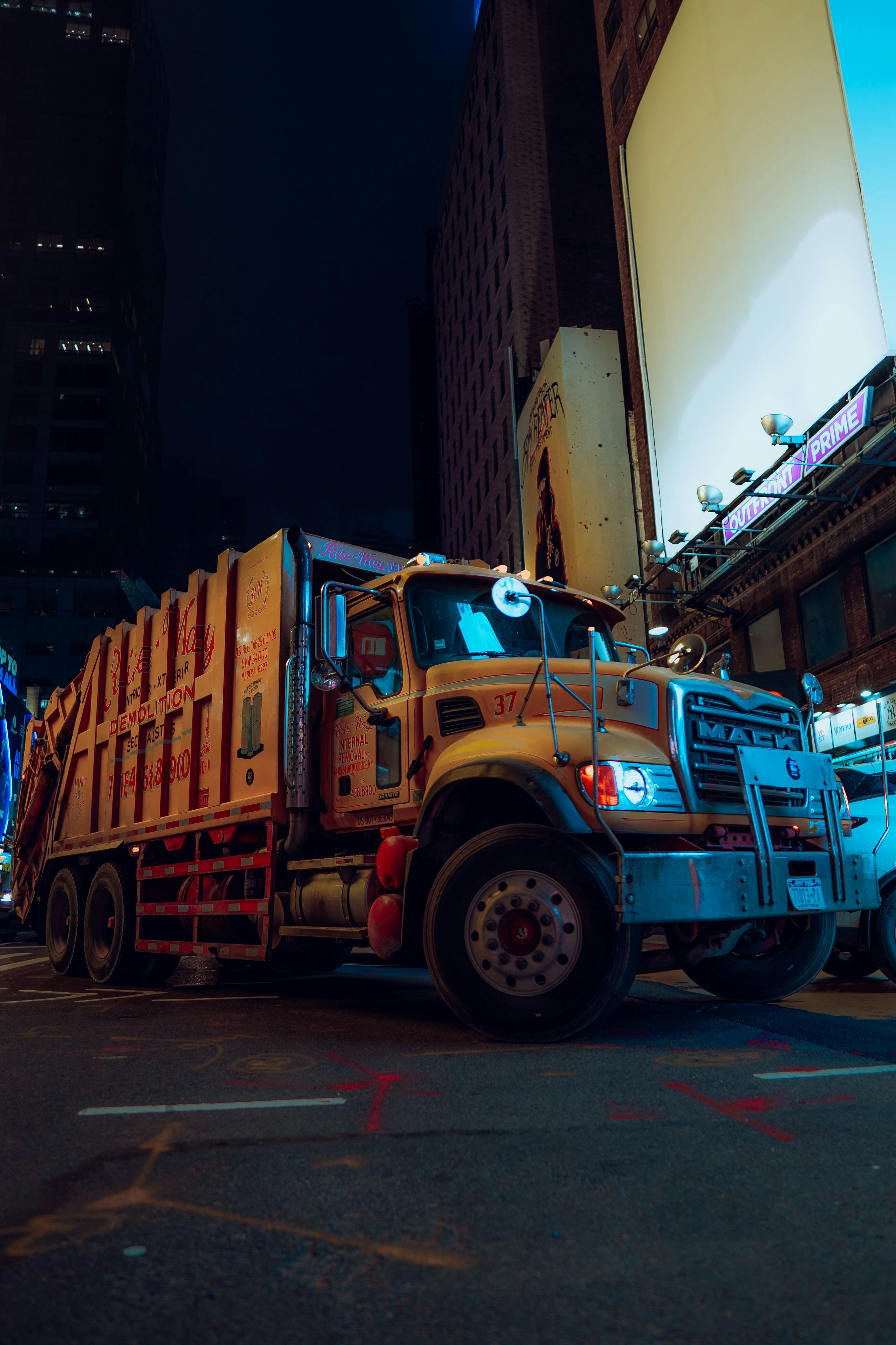 A garbage truck is parked on the street at night · Free Stock Photo