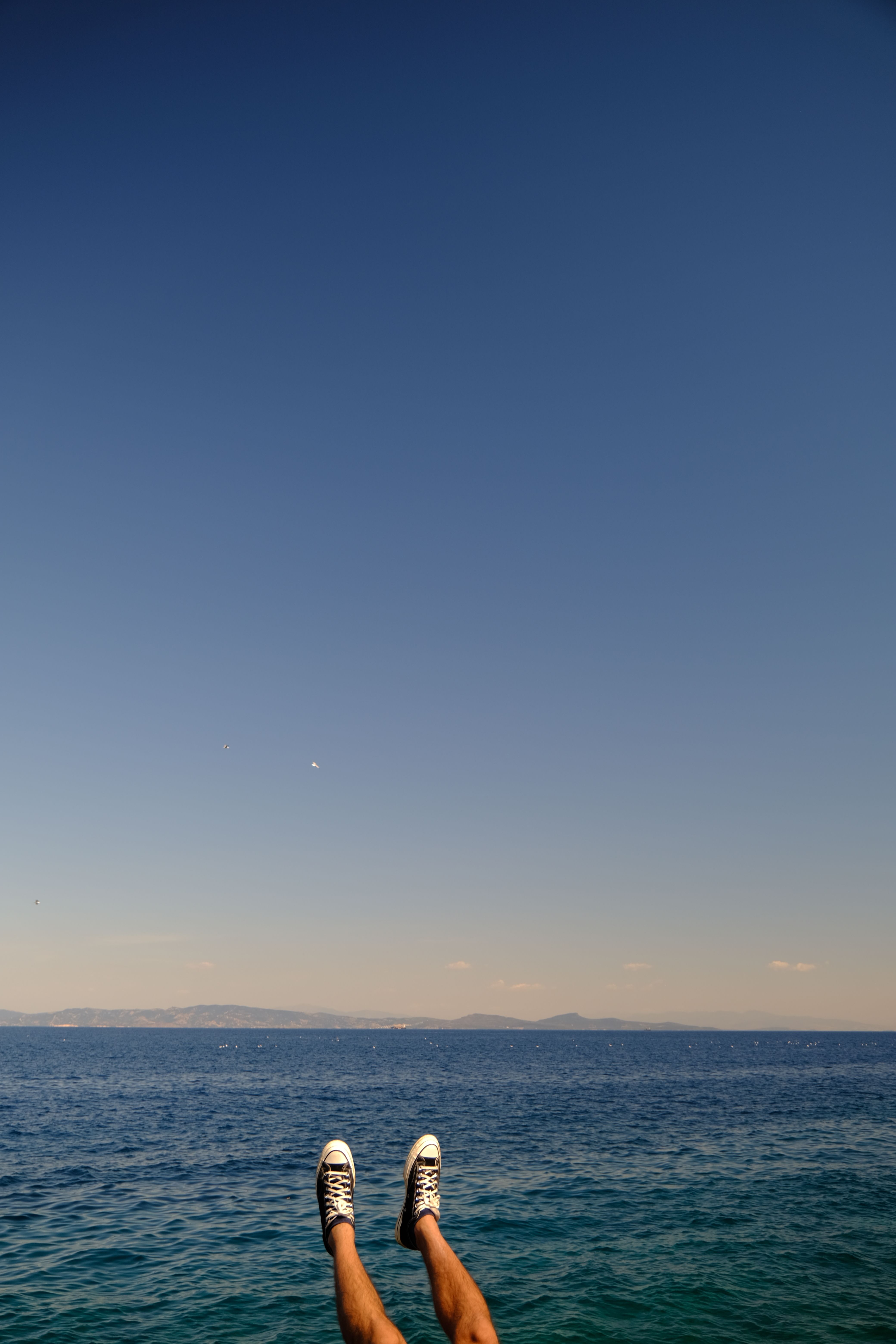 Legs with Sneakers on in the Front of a Landscape of a Sea Under a ...