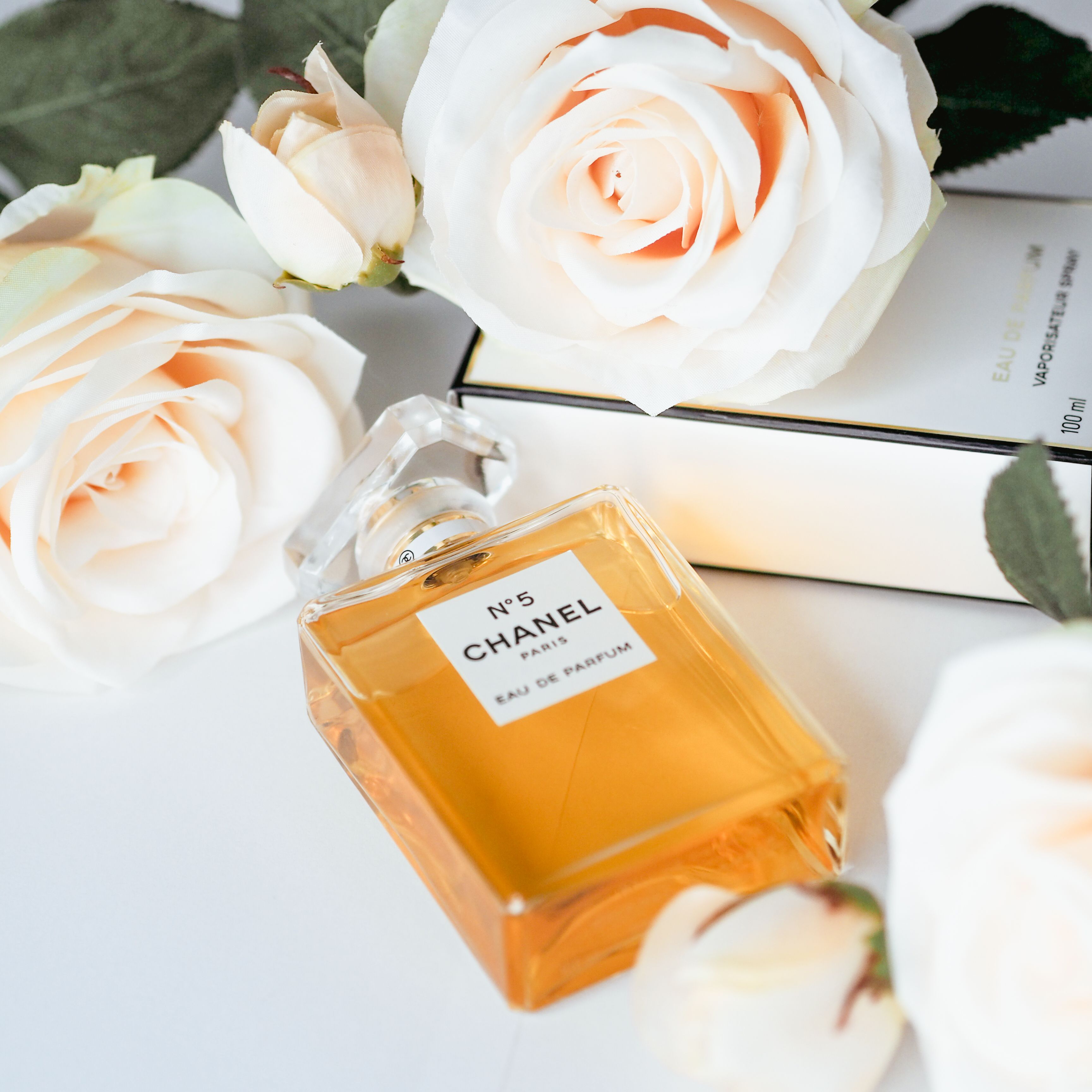 A Bottle of Chanel No 5 Perfume Lying on a White Surface with Flowers ...
