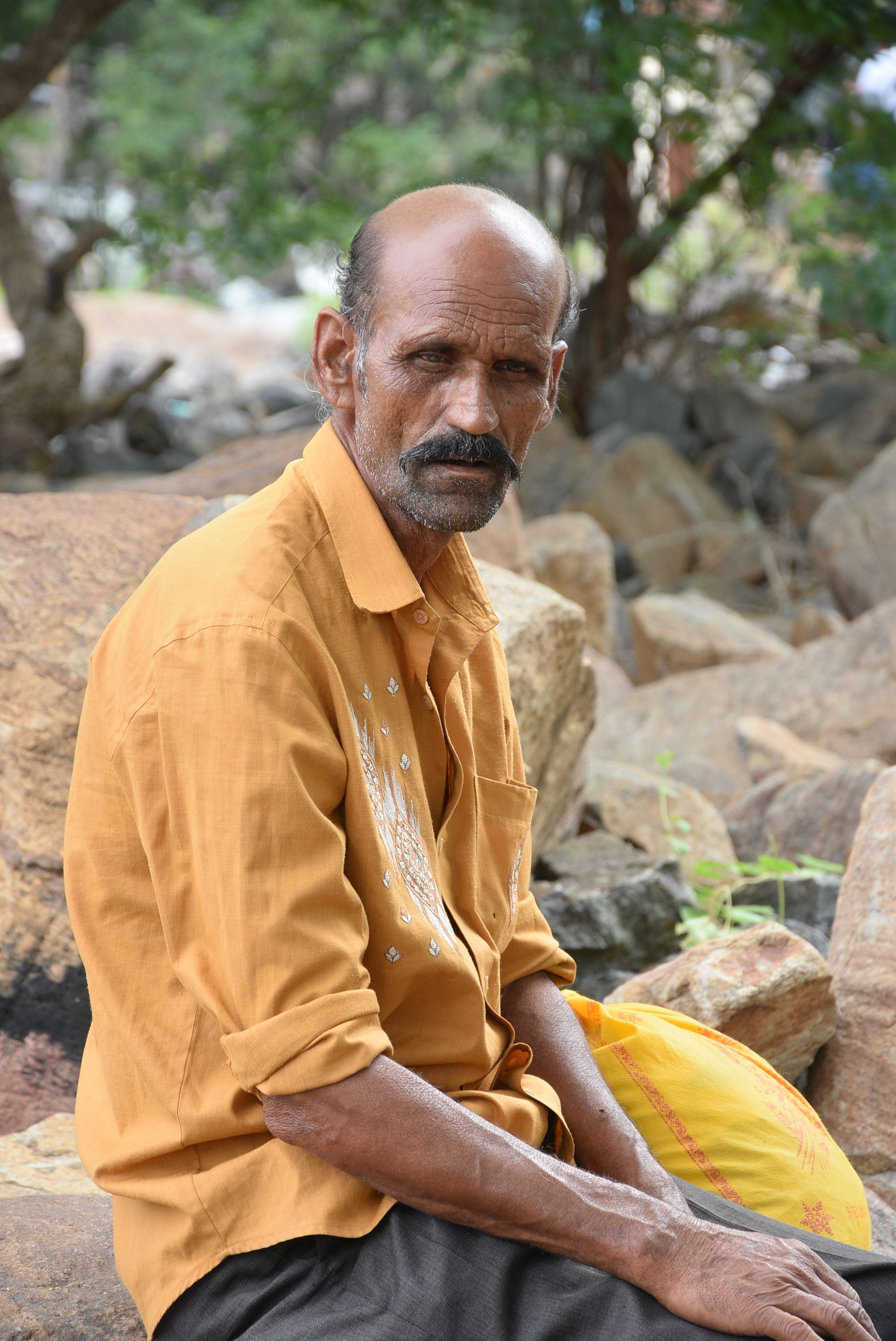 A Bald Man with Mustache Sitting on a Rock · Free Stock Photo