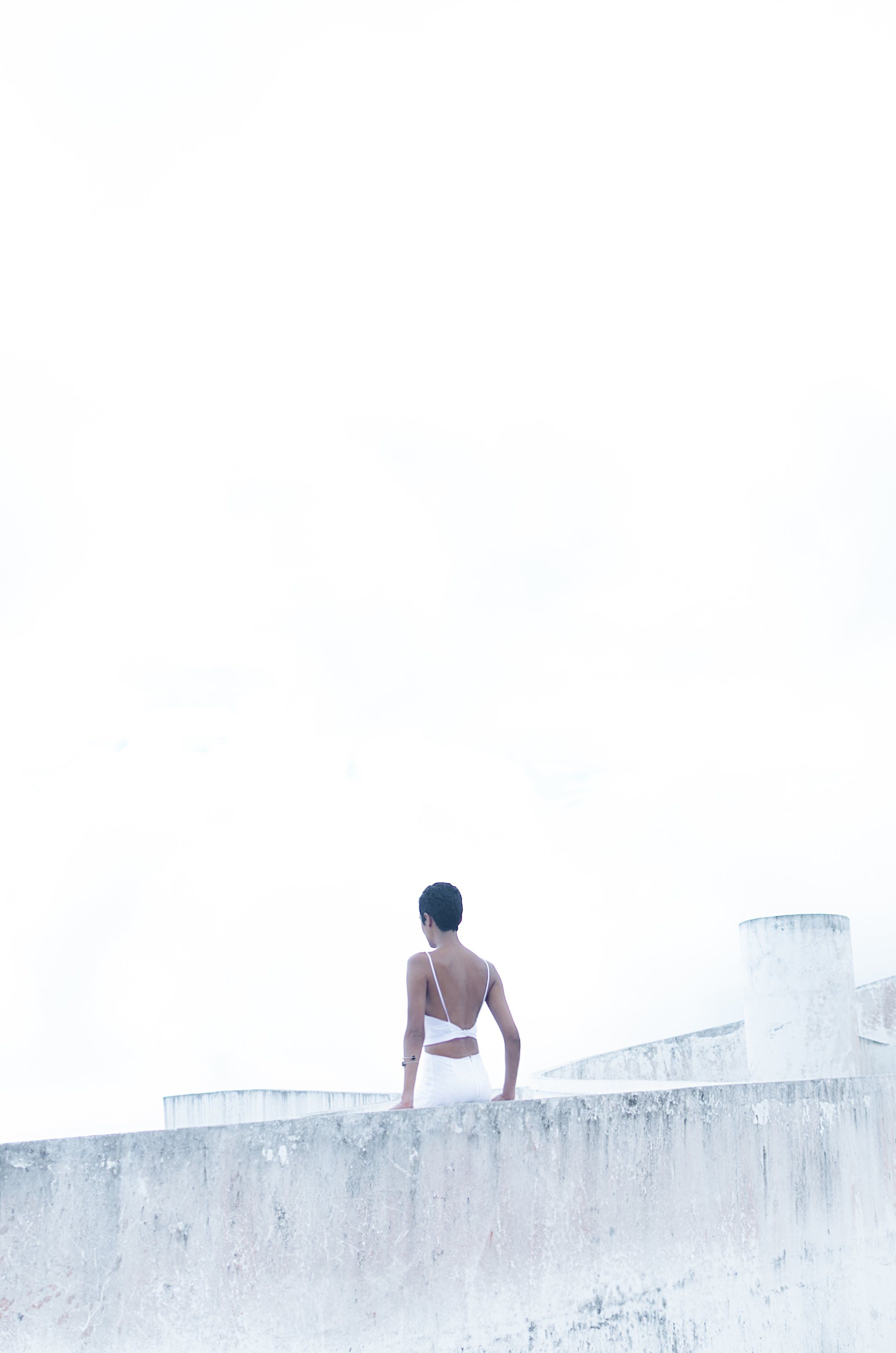 A woman standing on a ledge looking out over the ocean · Free Stock Photo